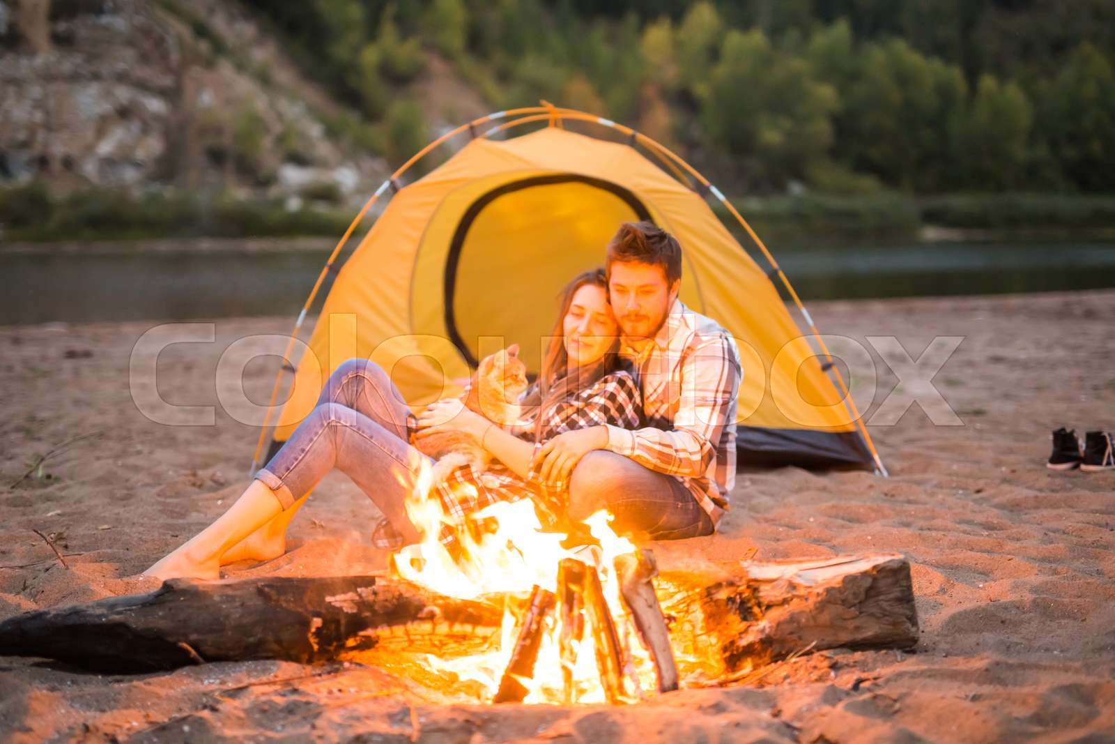 people, summer tourism and nature concept - couple near camp fire ...