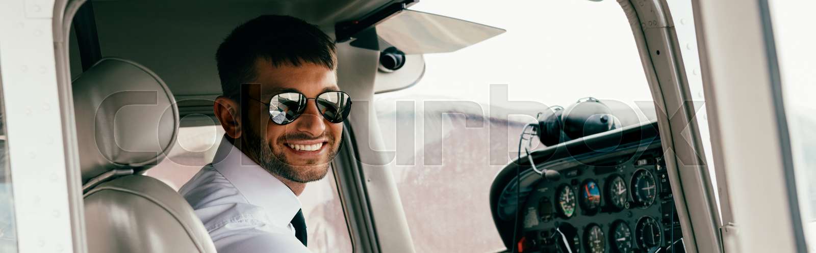 panoramic shot of smiling handsome pilot in sunglasses looking at ...