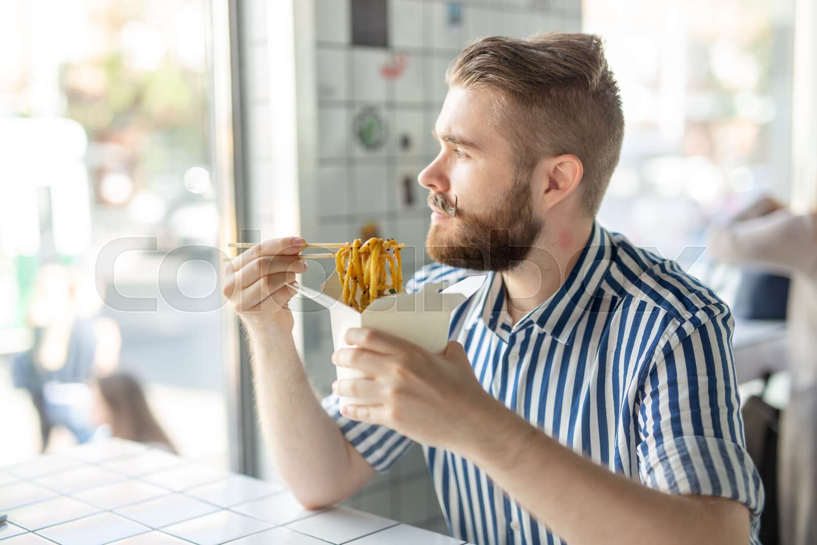 Side view of a handsome young hipster guy eating chinese noodles using ...