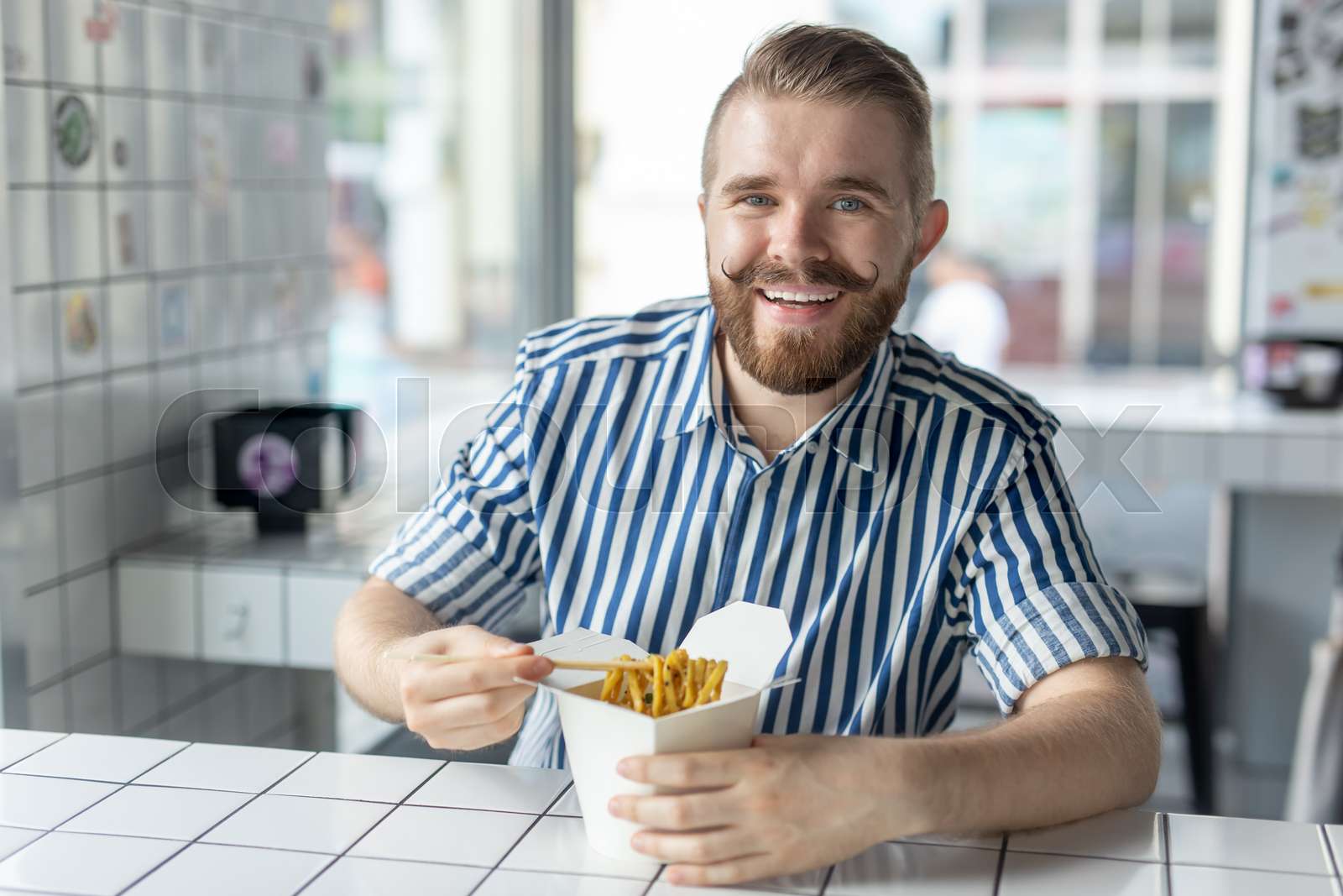 Positive young stylish guy eating chinese noodles in a cafe during a ...
