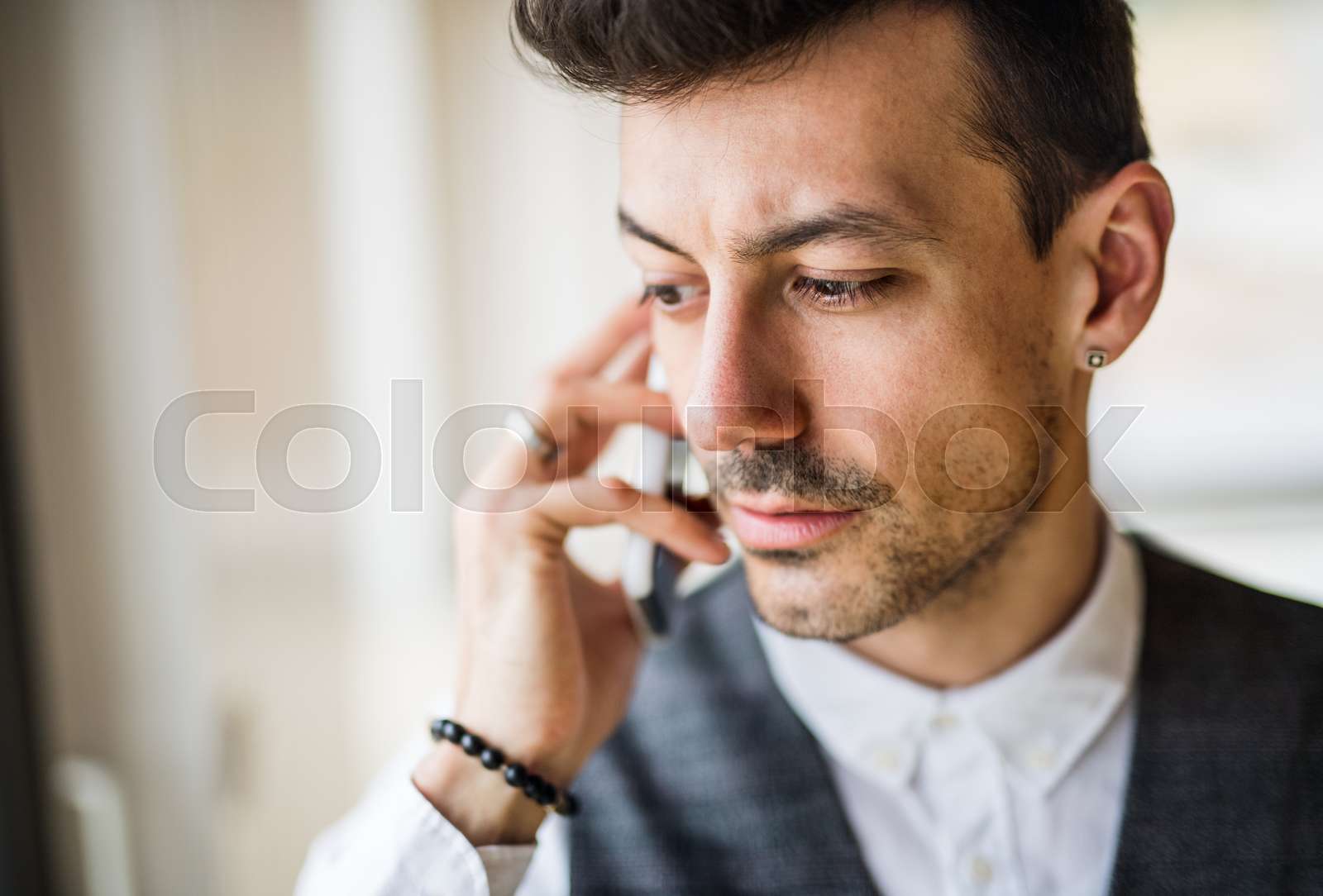 Young man with smartphone standing indoors at home, making a phone call ...