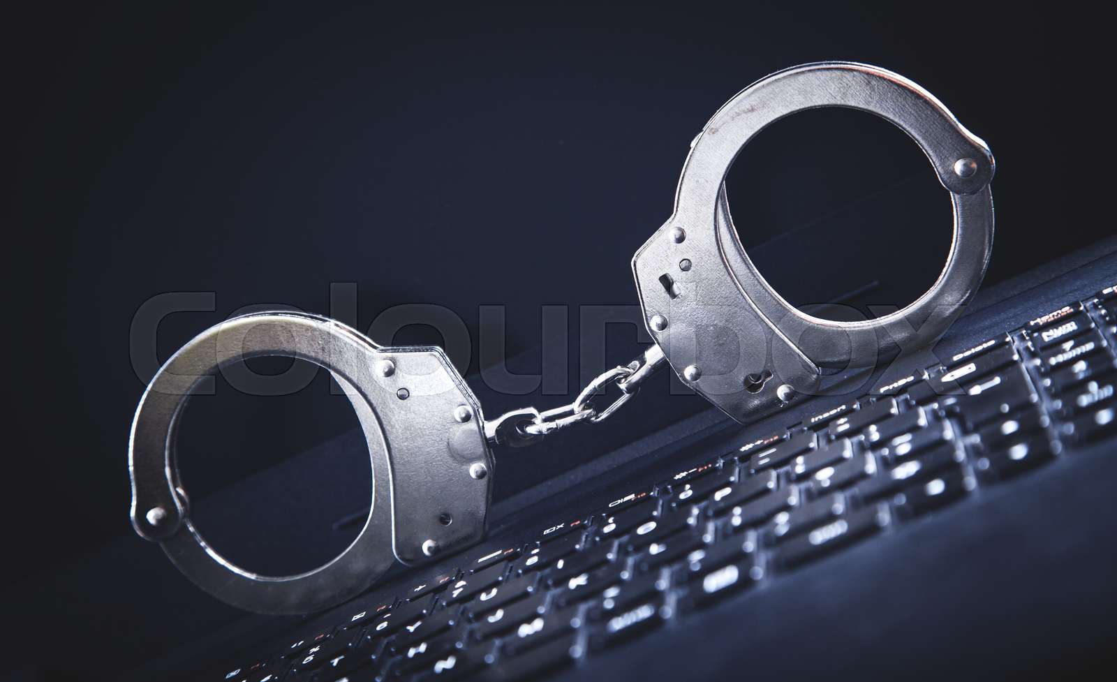 Handcuffs on computer keyboard. Cyber crime | Stock image | Colourbox