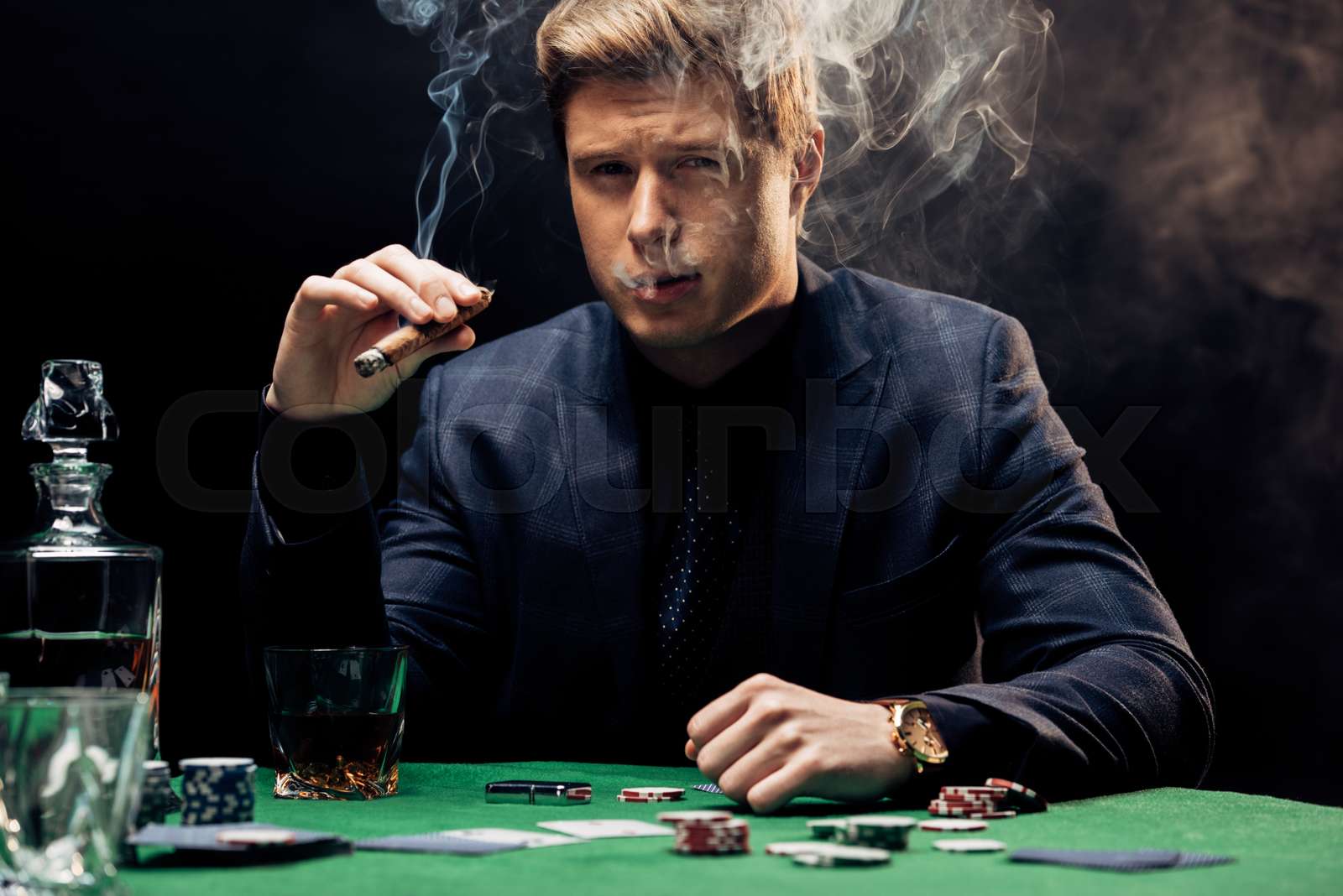 handsome man smoking cigar near poker table on black with smoke | Stock ...