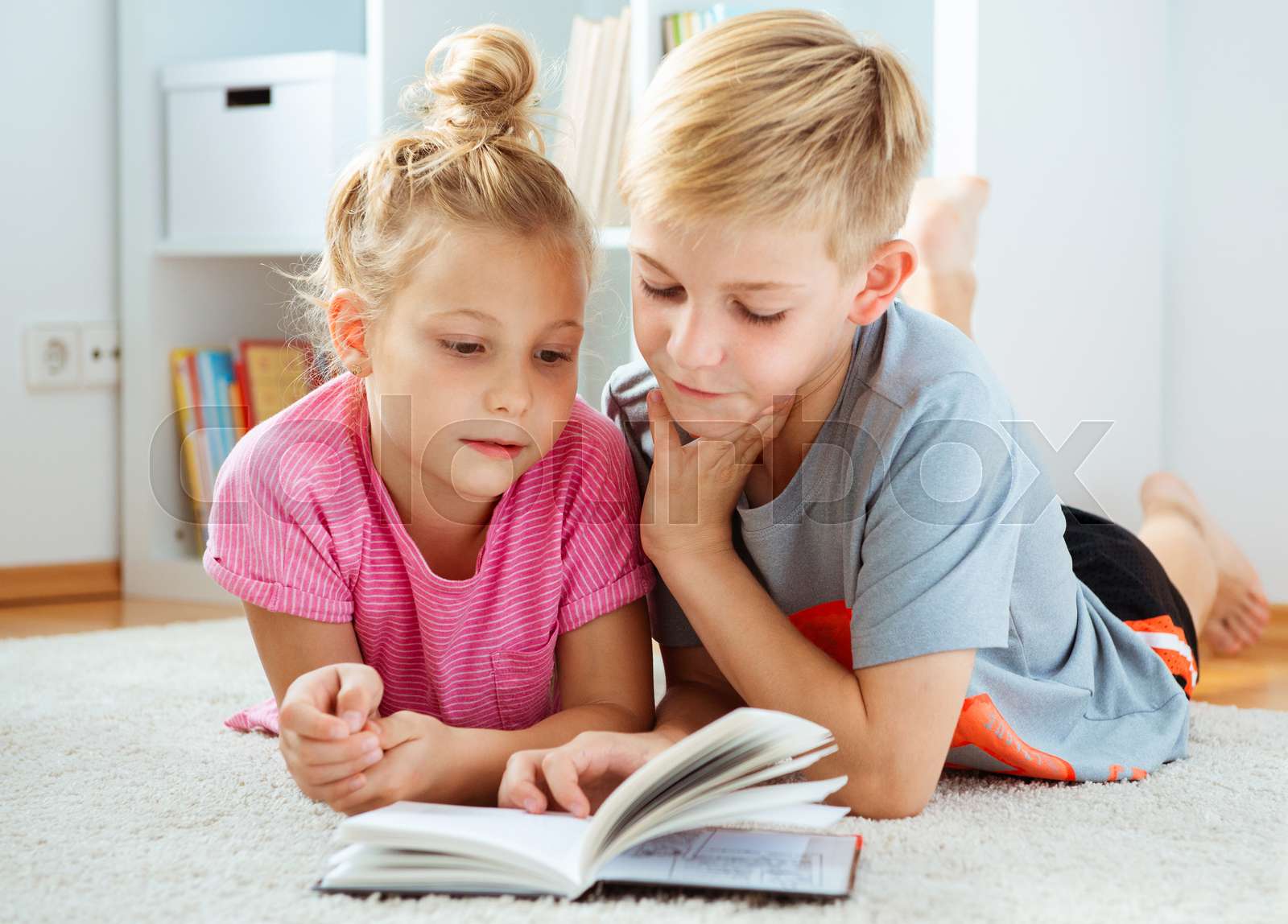 Portrait of two children reading a book on the floor at home | Stock ...