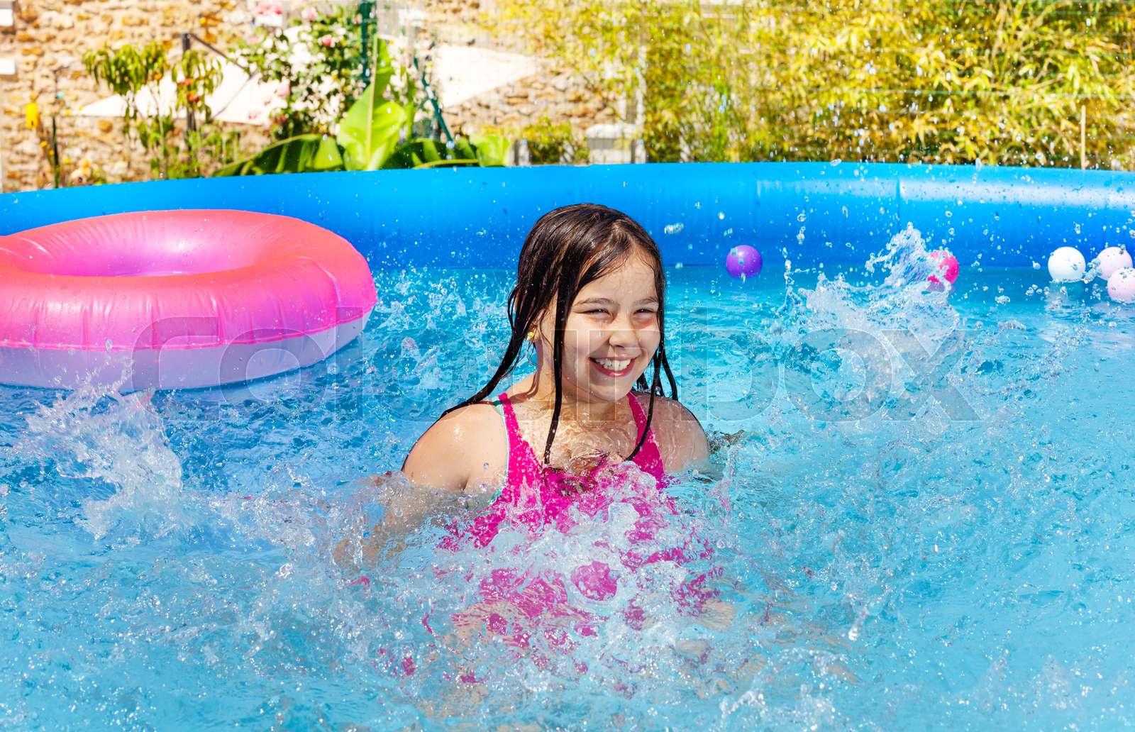 Happy little girl splash water in swimming pool | Stock image | Colourbox