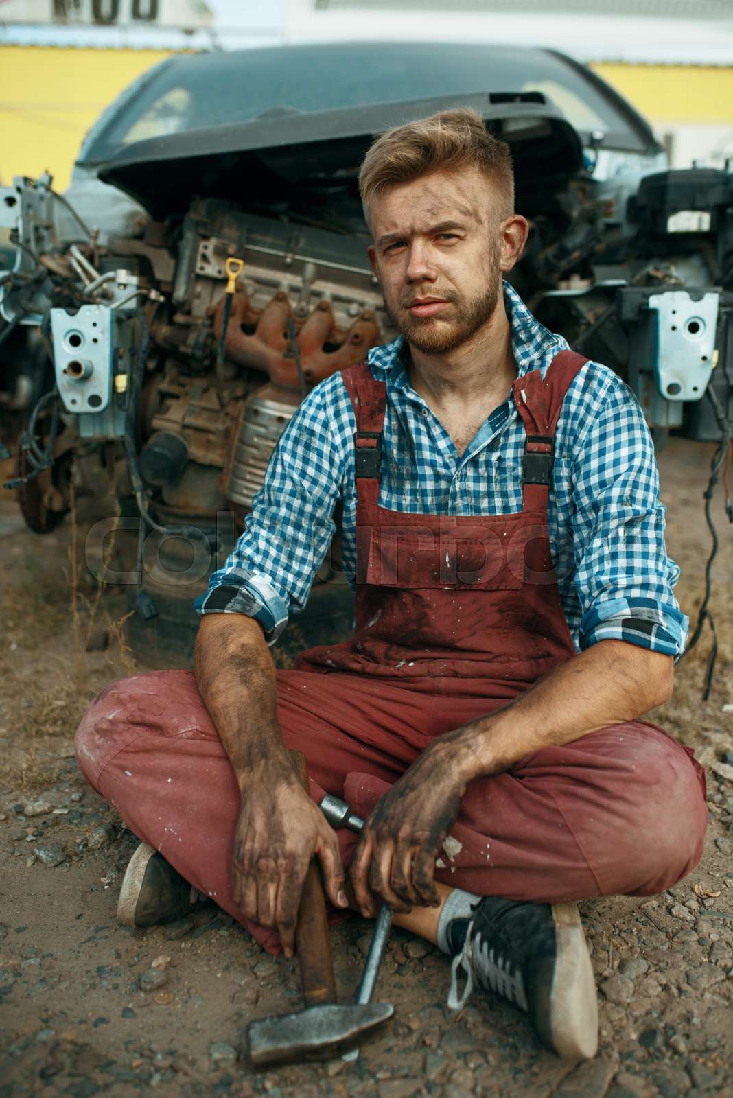 Male repairman sitting on the ground, car junkyard | Stock image ...