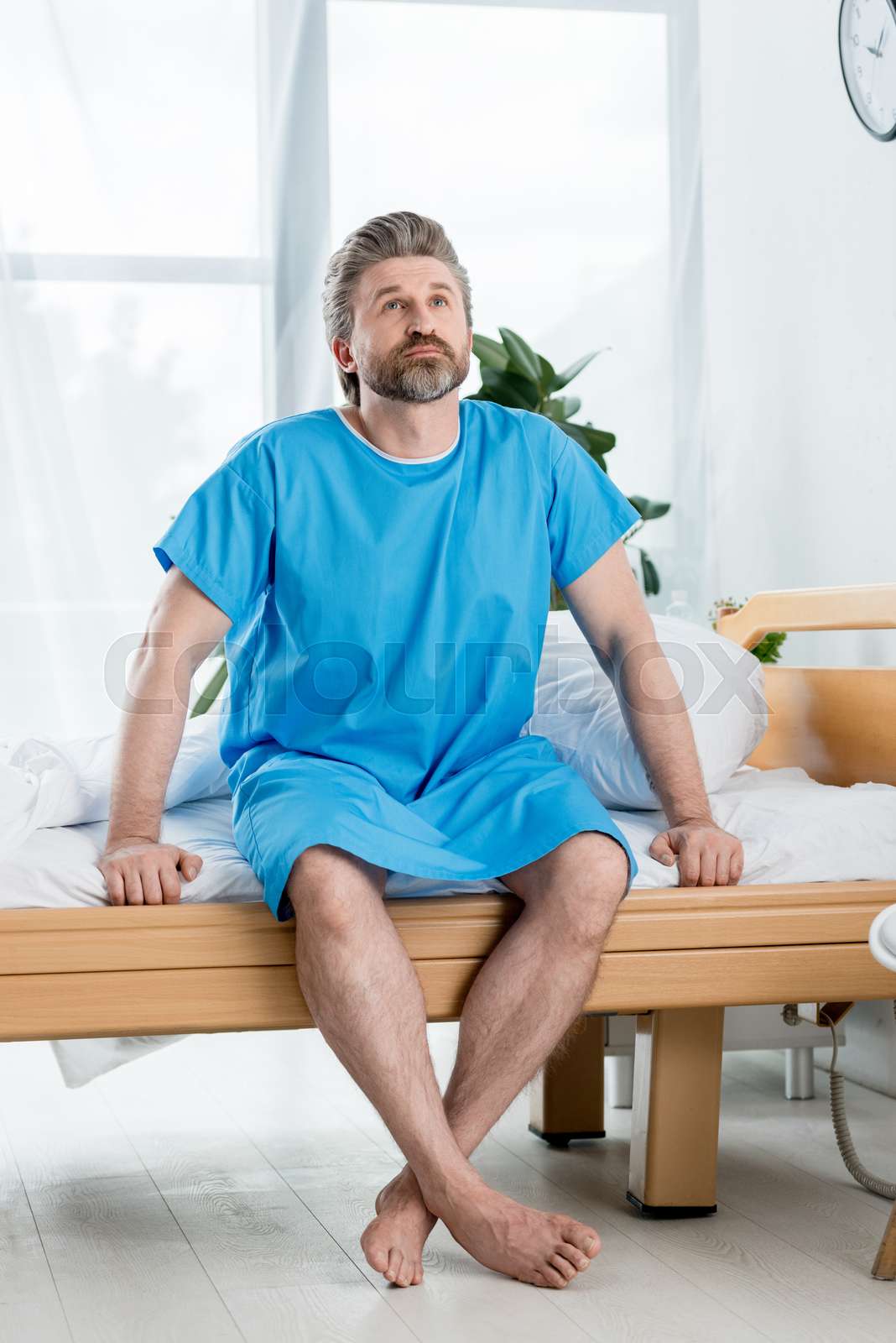 patient in medical gown sitting on bed and looking up in hospital ...