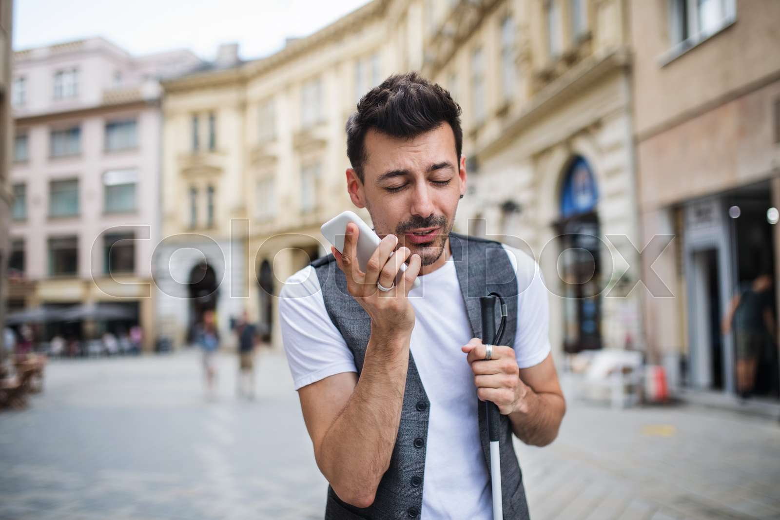 Young blind man with smartphone on street in city, making phone call ...