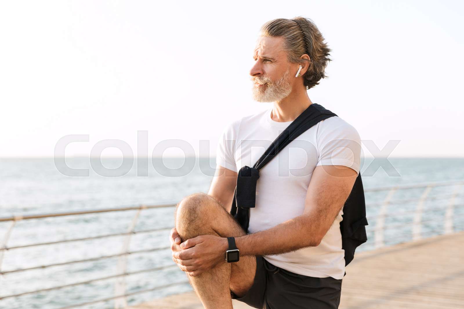 Image of thinking old man using earpod while stretching his leg | Stock ...