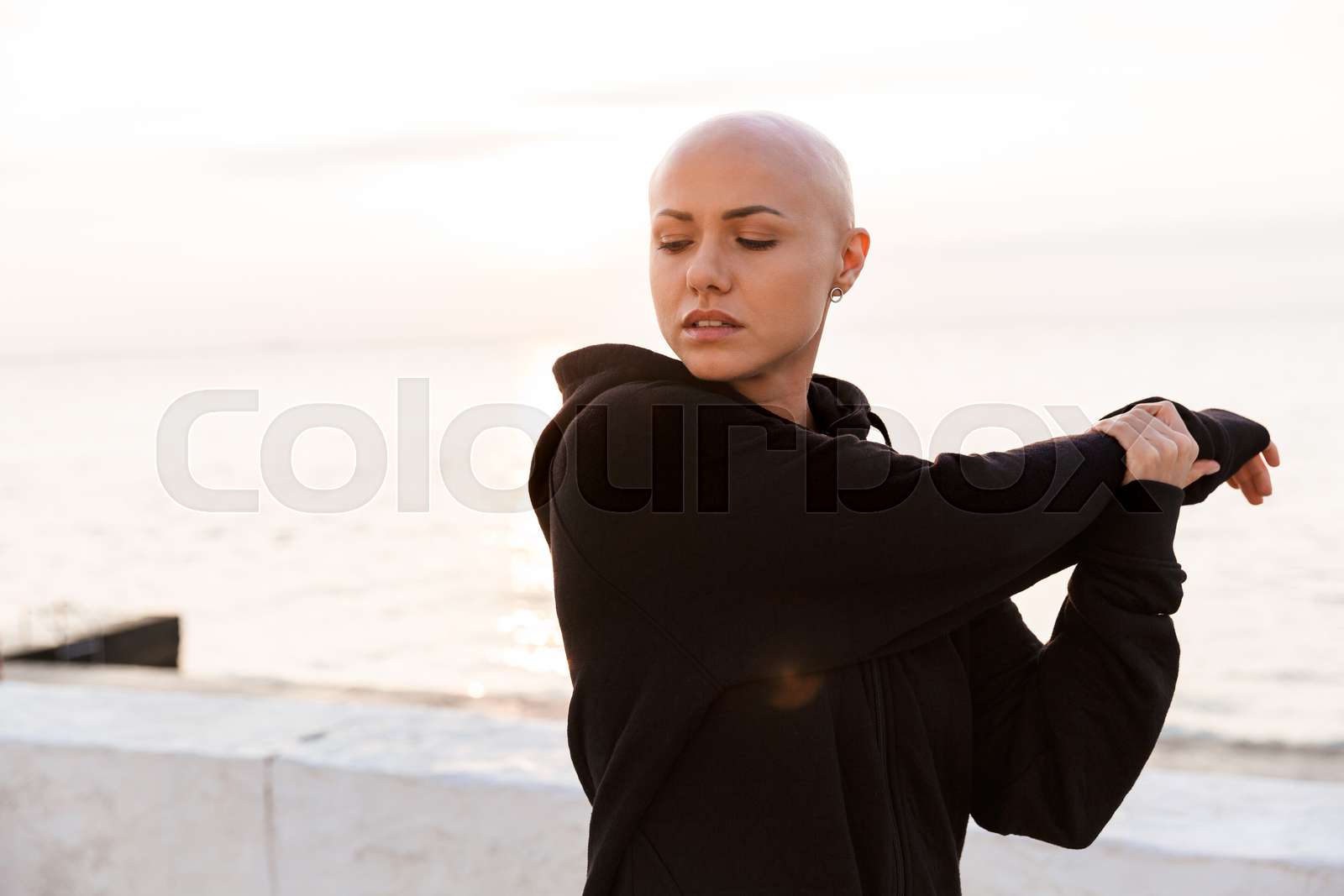 Image of focused bald woman looking downward and stretching arms ...