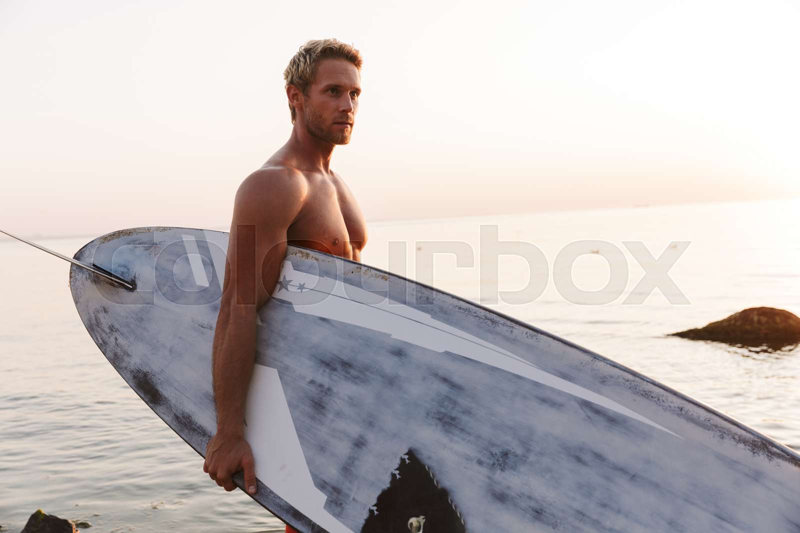 Image of shirtless surfer man holding his surfboard by ocean at sunrise ...