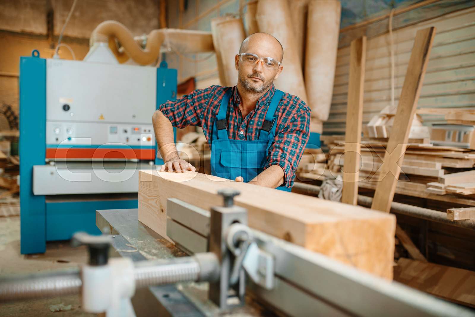 Carpenter processes wooden beam on plane machine | Stock image | Colourbox