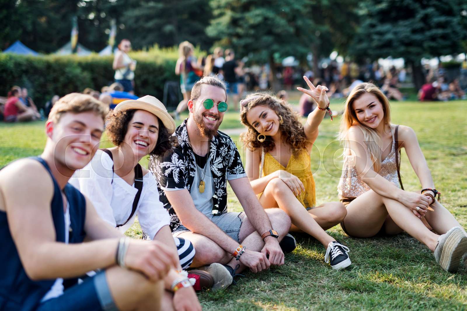 Group of young friends sitting on ground at summer festival. | Stock ...