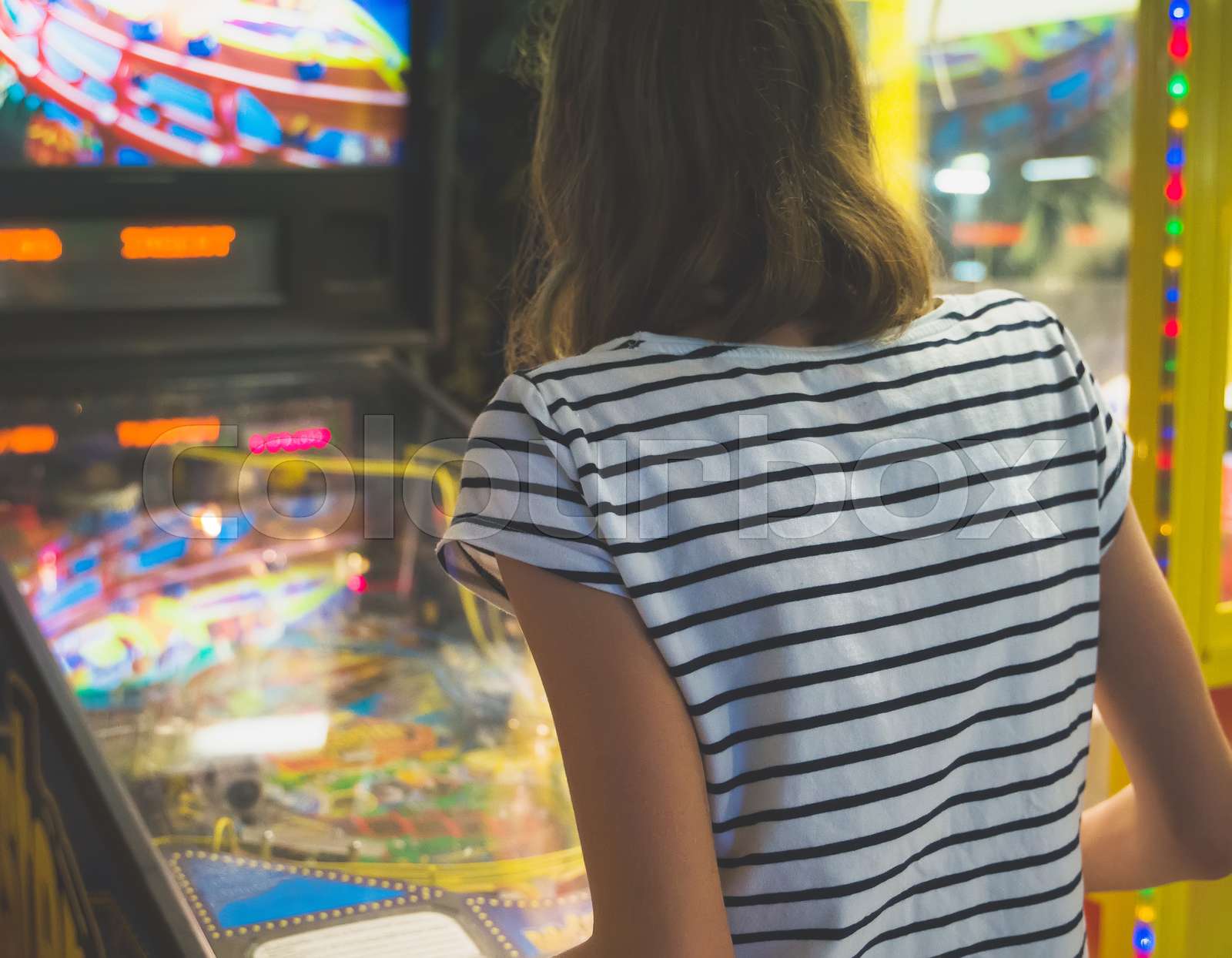 Little girl playing pinball game in theme park. | Stock image | Colourbox