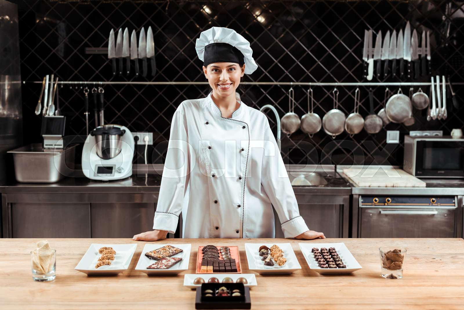 happy chocolatier standing near tasty chocolate candies on plates ...