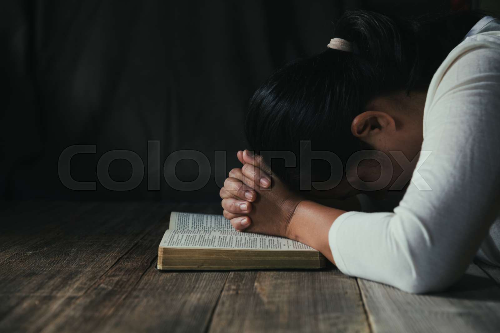 Hands folded in prayer on a Holy Bible in church concept for faith ...