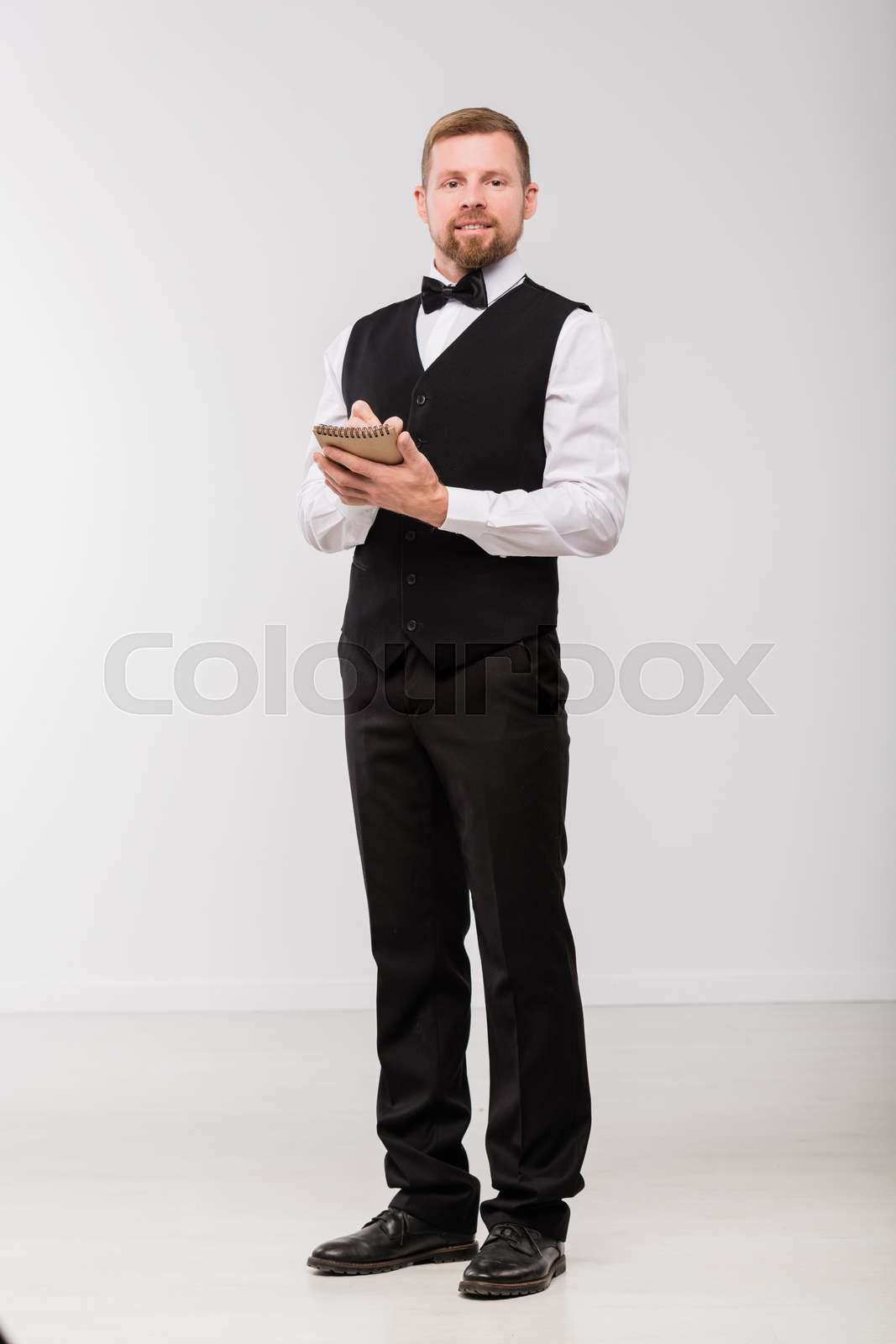 Young elegant waiter with notepad and pen writing down order of one of ...