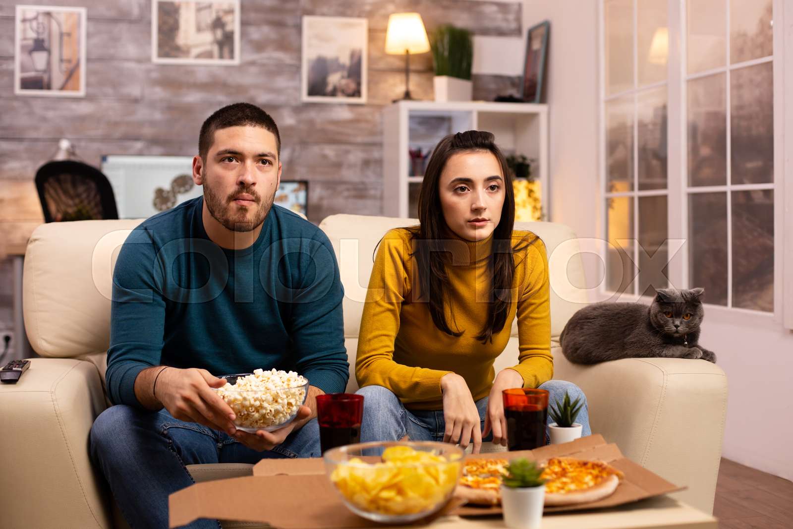 Beautiful young couple watching TV and eating fast food takeaway ...