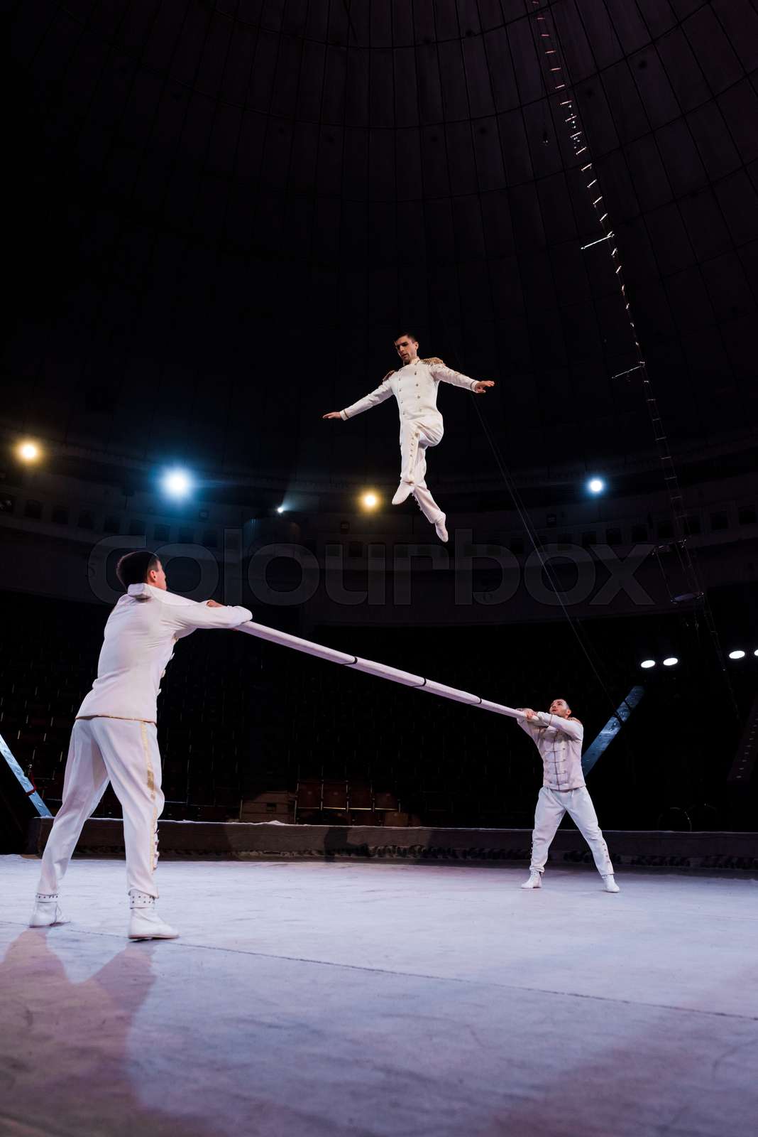 acrobats holding pole near gymnast jumping in circus | Stock image ...