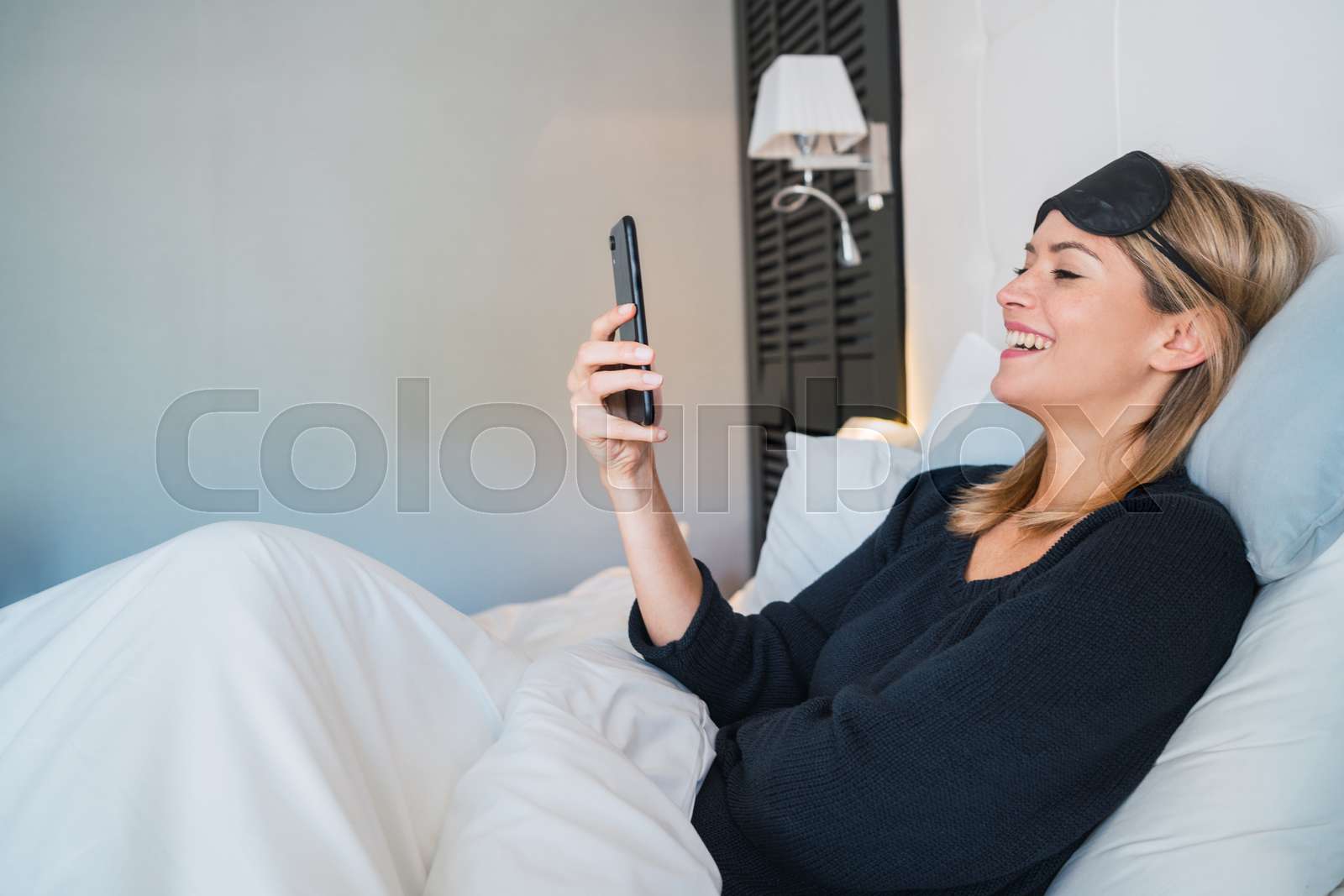 Young woman using her phone while laying on bed. | Stock image | Colourbox