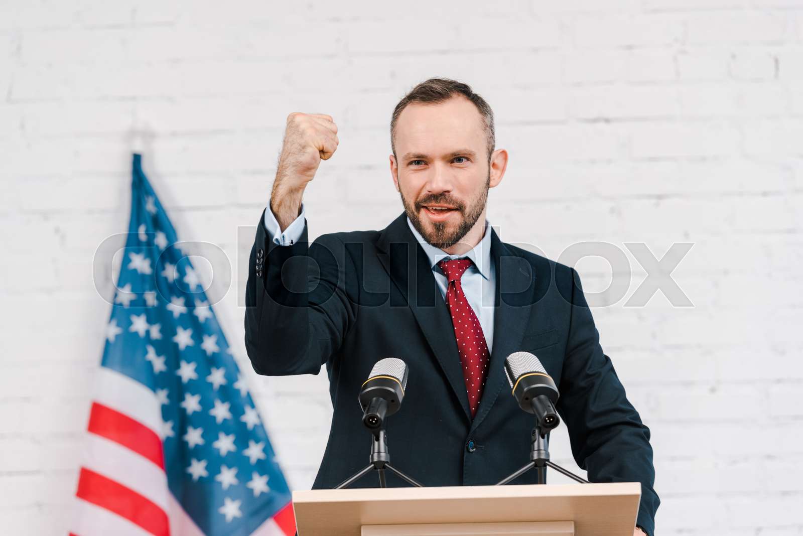 selective focus of emotional speaker with clenched fist talking near microphones and american ...