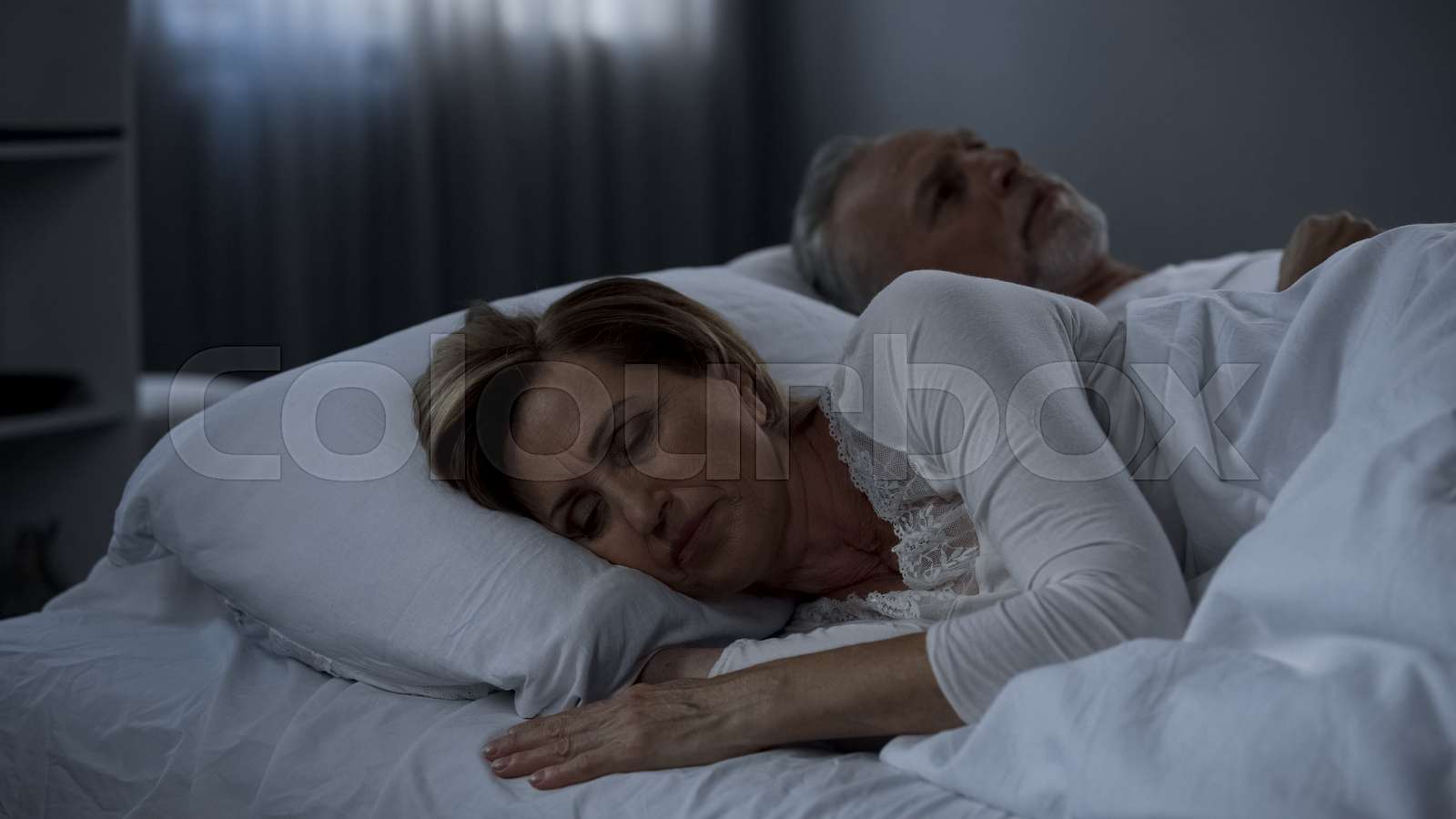 Aging husband and wife lying in bed awake, lady turned back to man, low ...