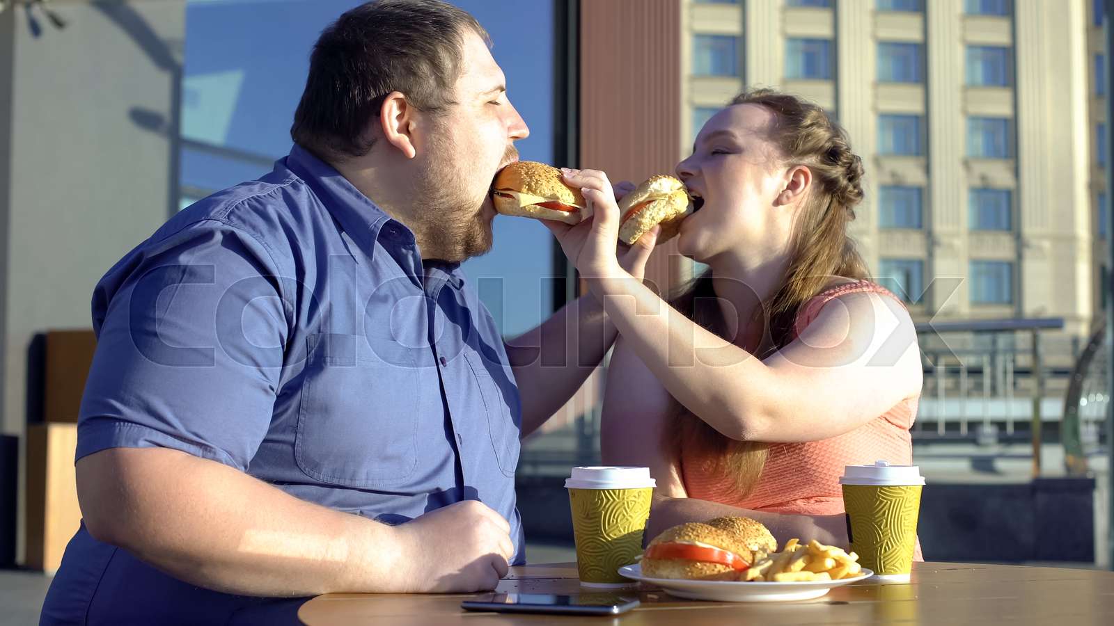 Oversize couple sharing burgers during romantic date outdoors, calories ...