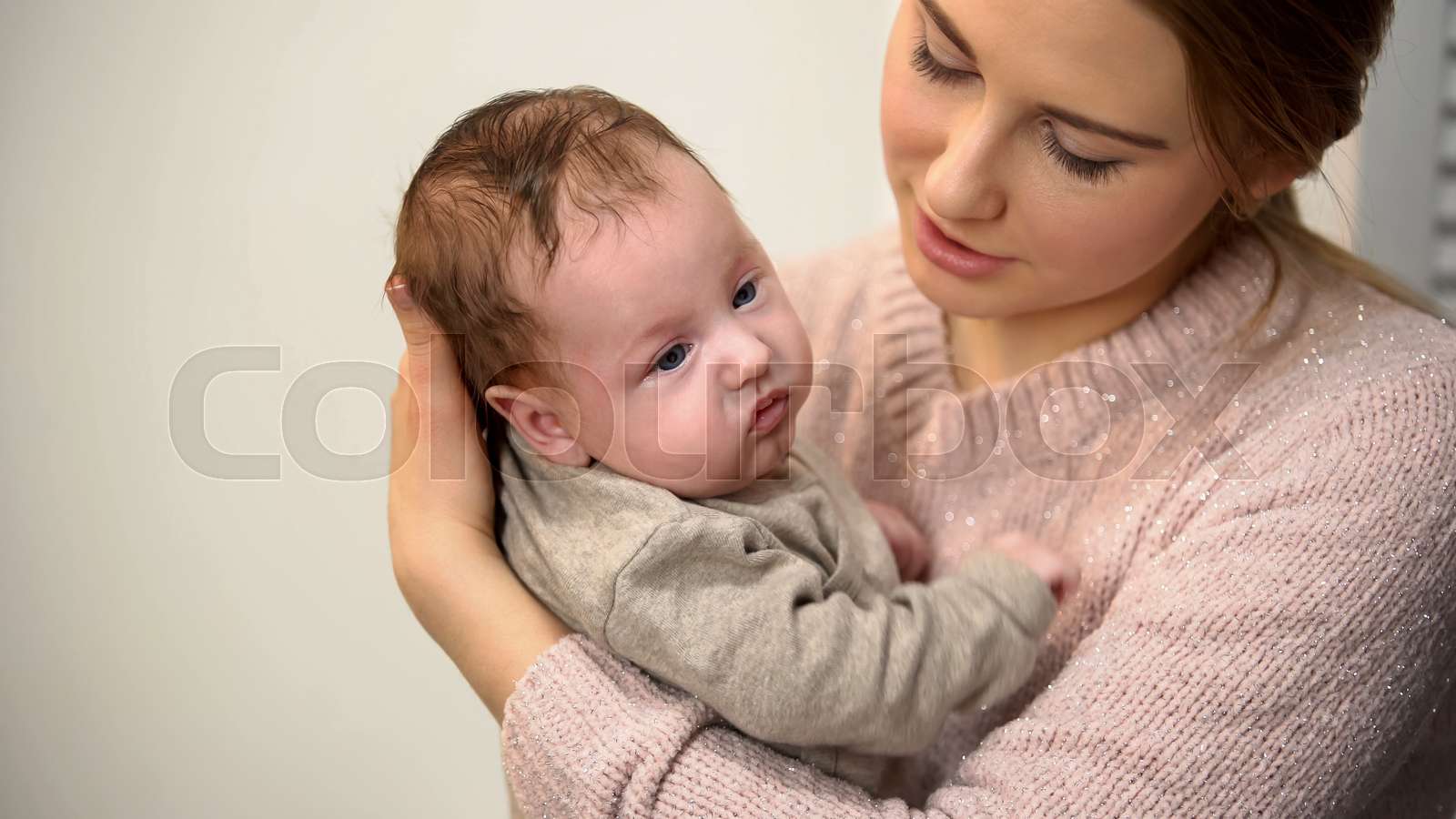 Attentive female babysitter holding little adorable baby and talking to ...