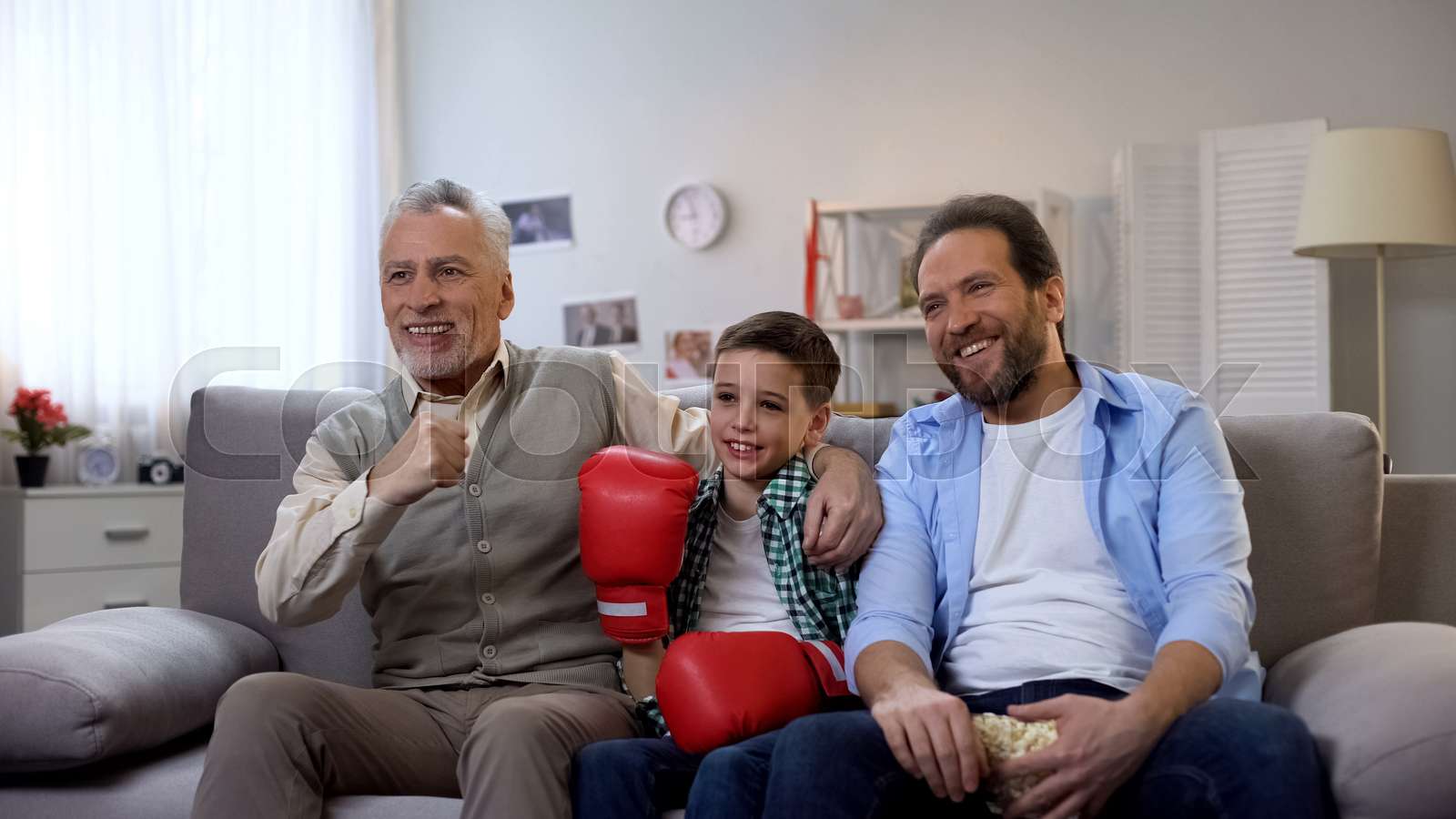 Smiling male family members watching boxing on tv, cheering for ...