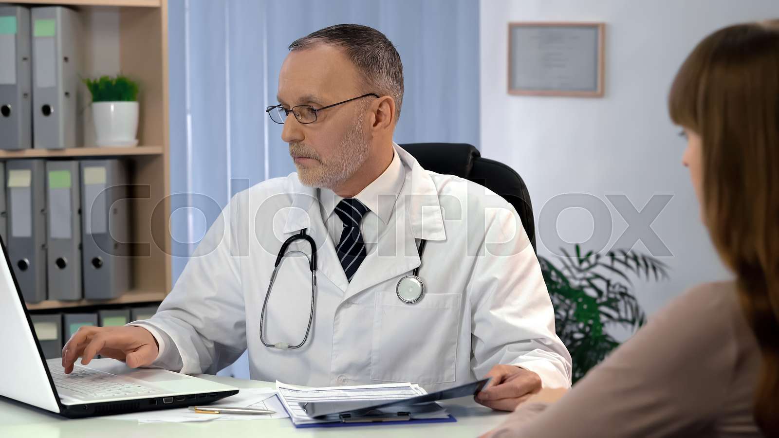Doctor checking analysis on laptop, holding x-ray, digital devices ...
