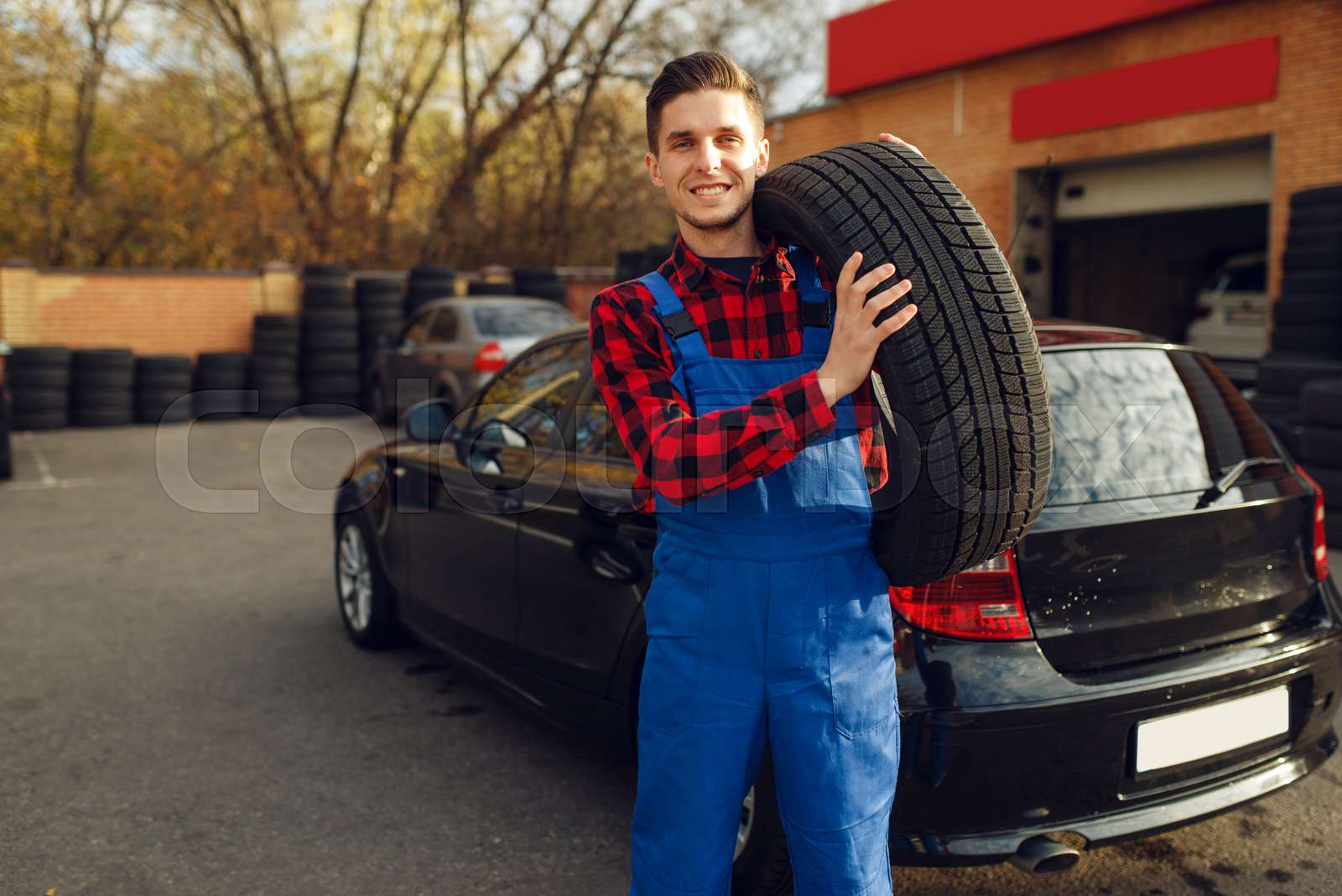 Male worker in uniform holds tyre, tire service | Stock image | Colourbox