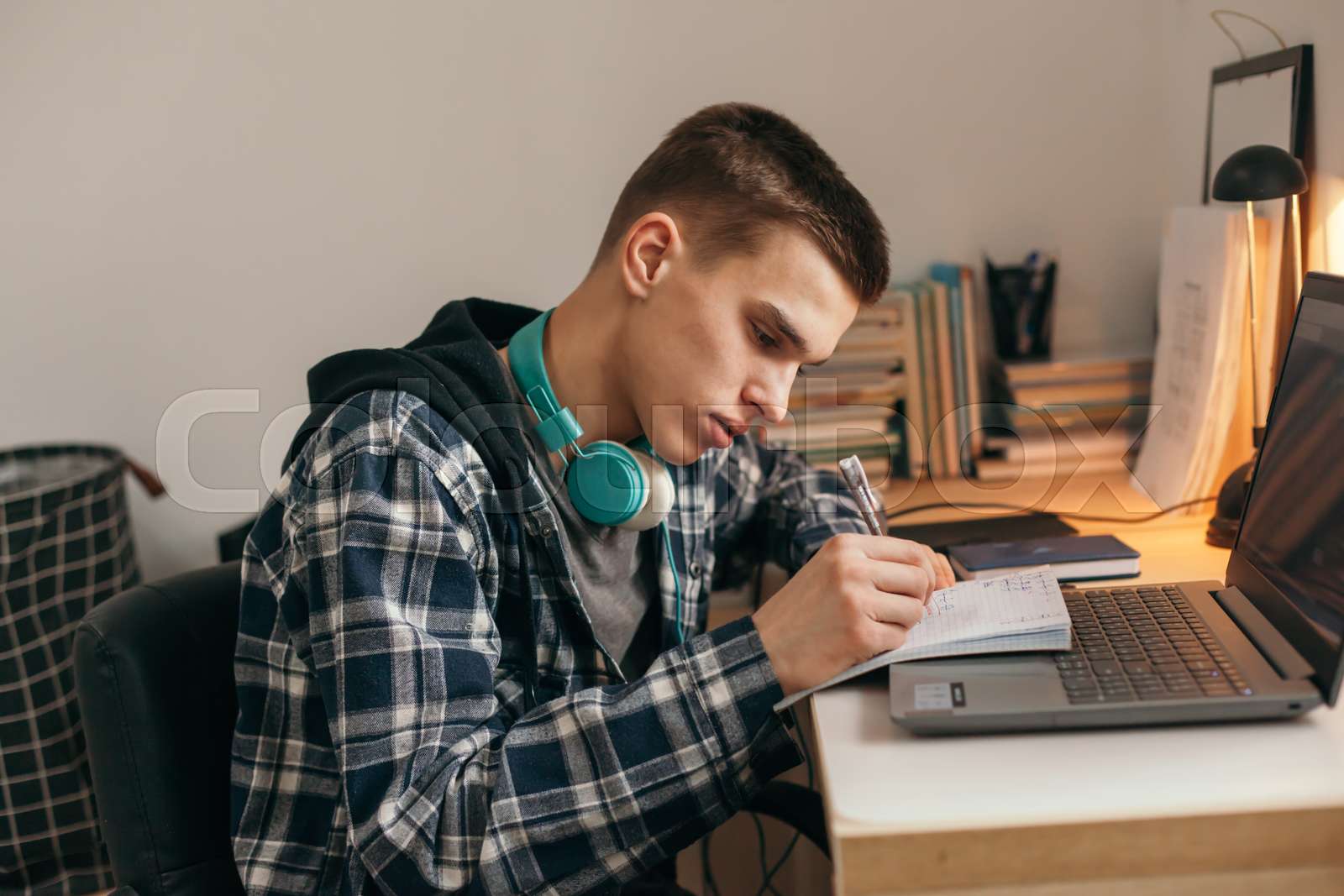 Teenage boy doing homework using computer sitting by desk in room alone ...