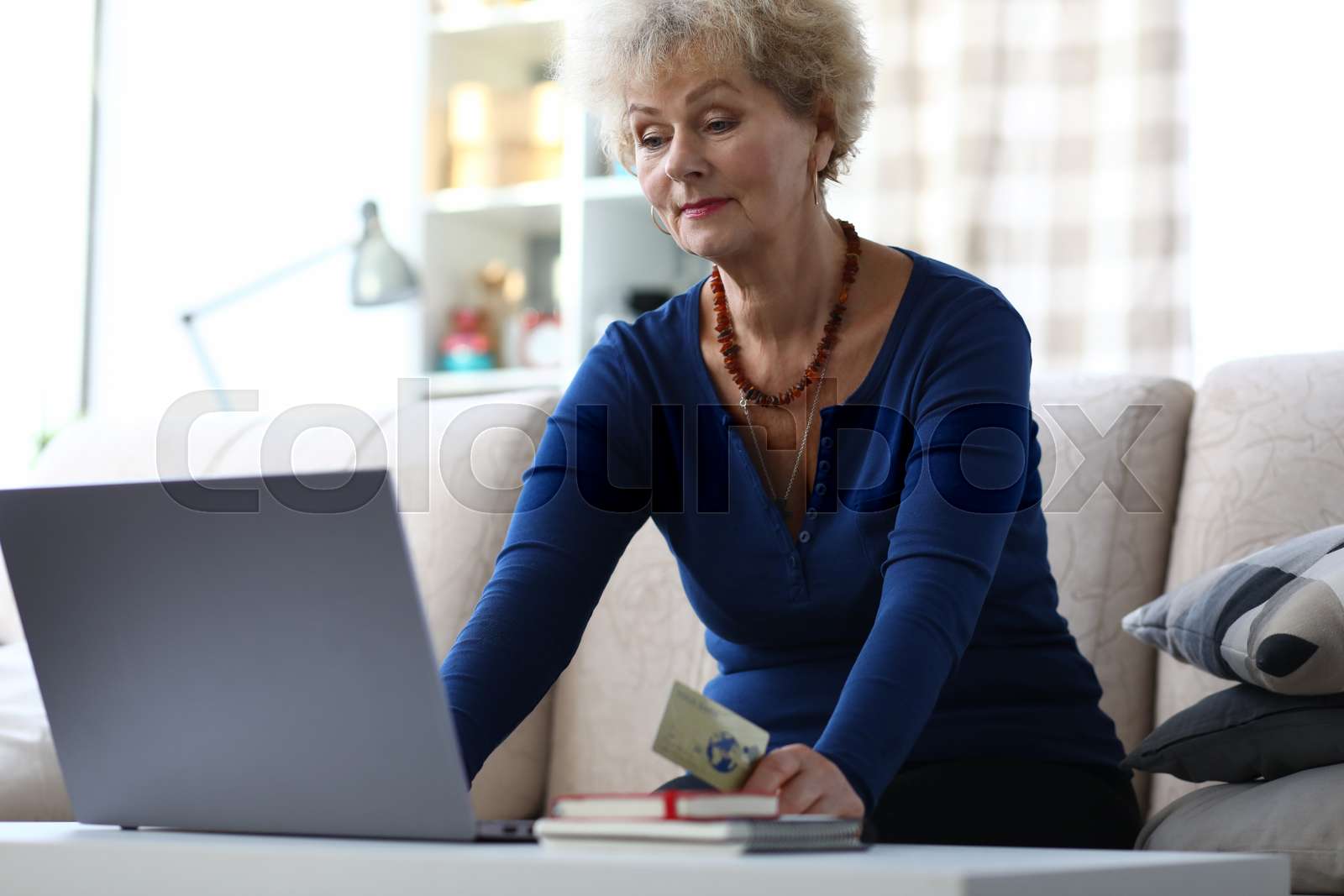 Elderly woman uses a bank card to pay online. | Stock image | Colourbox