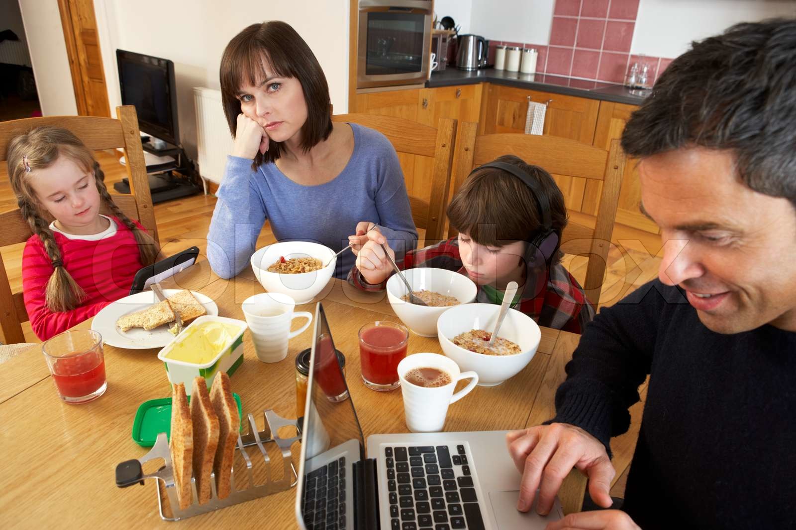 Family Using Gadgets Whilst Eating Breakfast Together In Kitchen ...