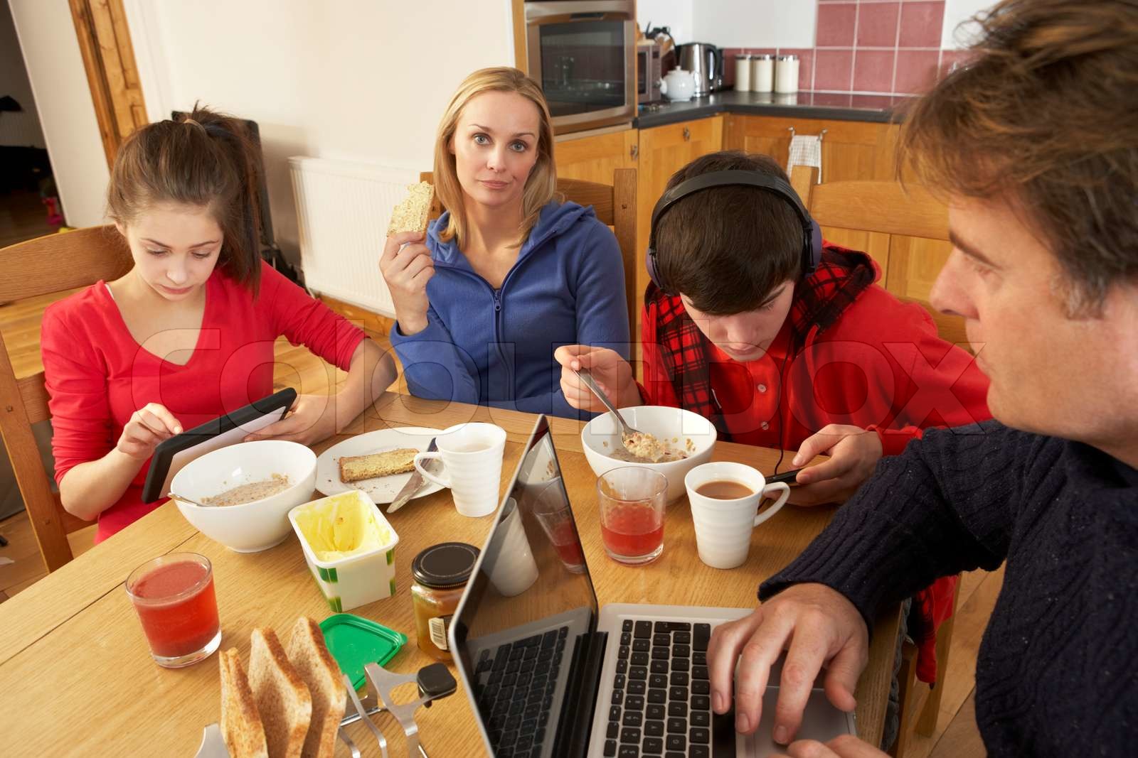 Teenage Family Using Gadgets Whilst Eating Breakfast Together In ...