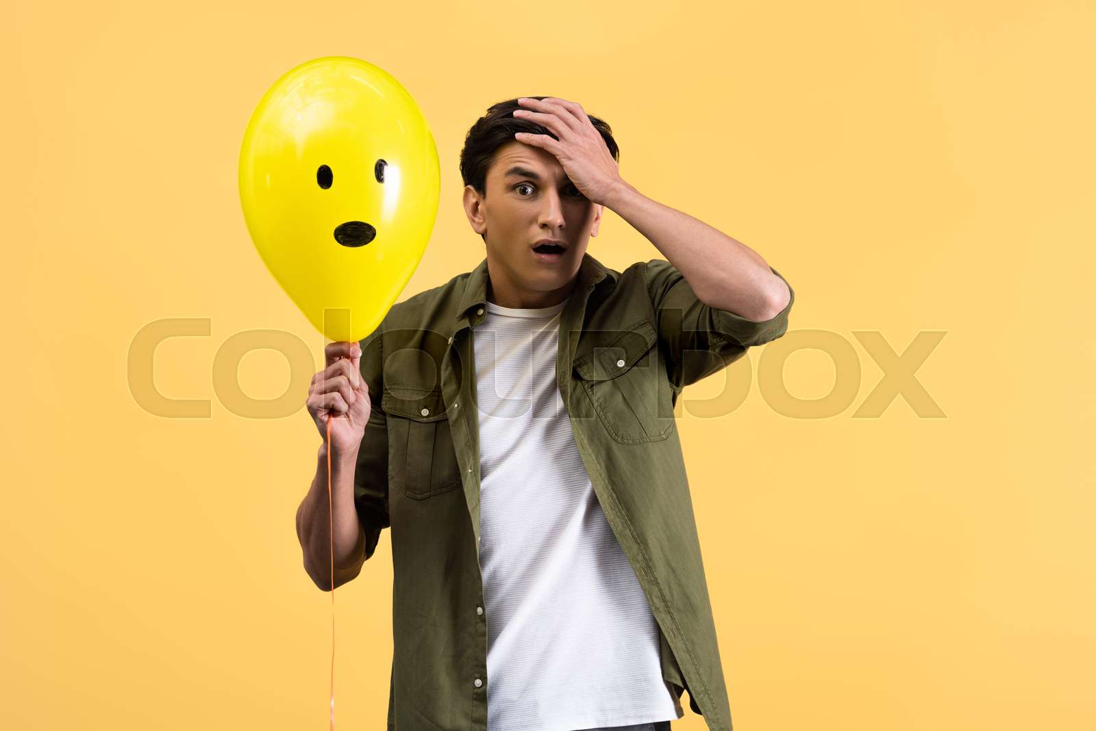 Worried young man holding shocked balloon, isolated on yellow | Stock ...