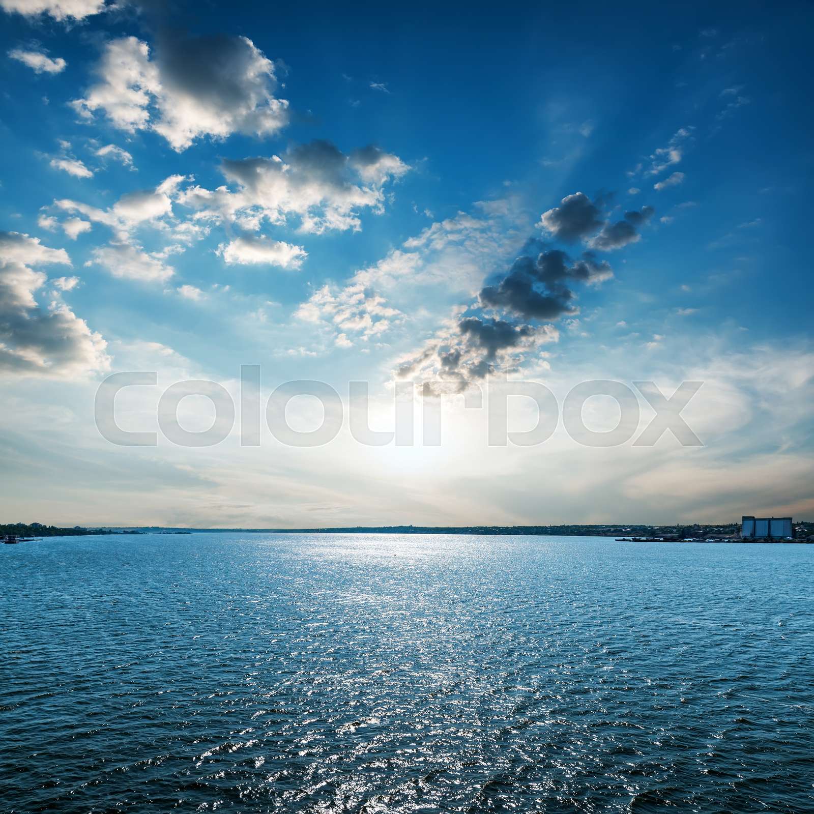 low sun in blue sky with clouds over dark water | Stock image | Colourbox
