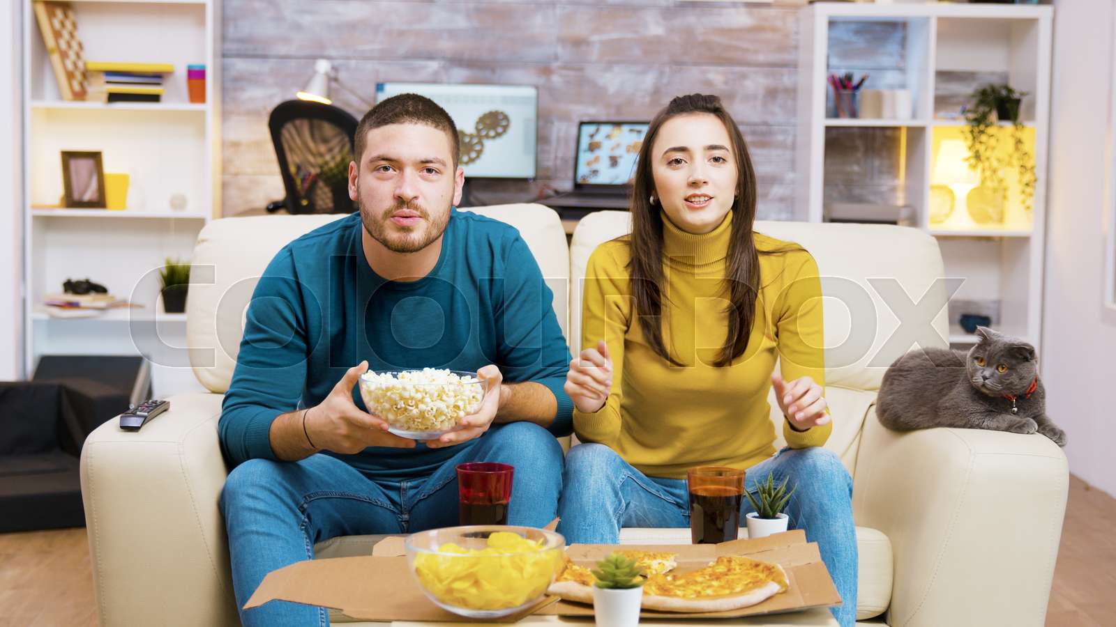 Excited couple sitting on the couch eating junk food | Stock image ...