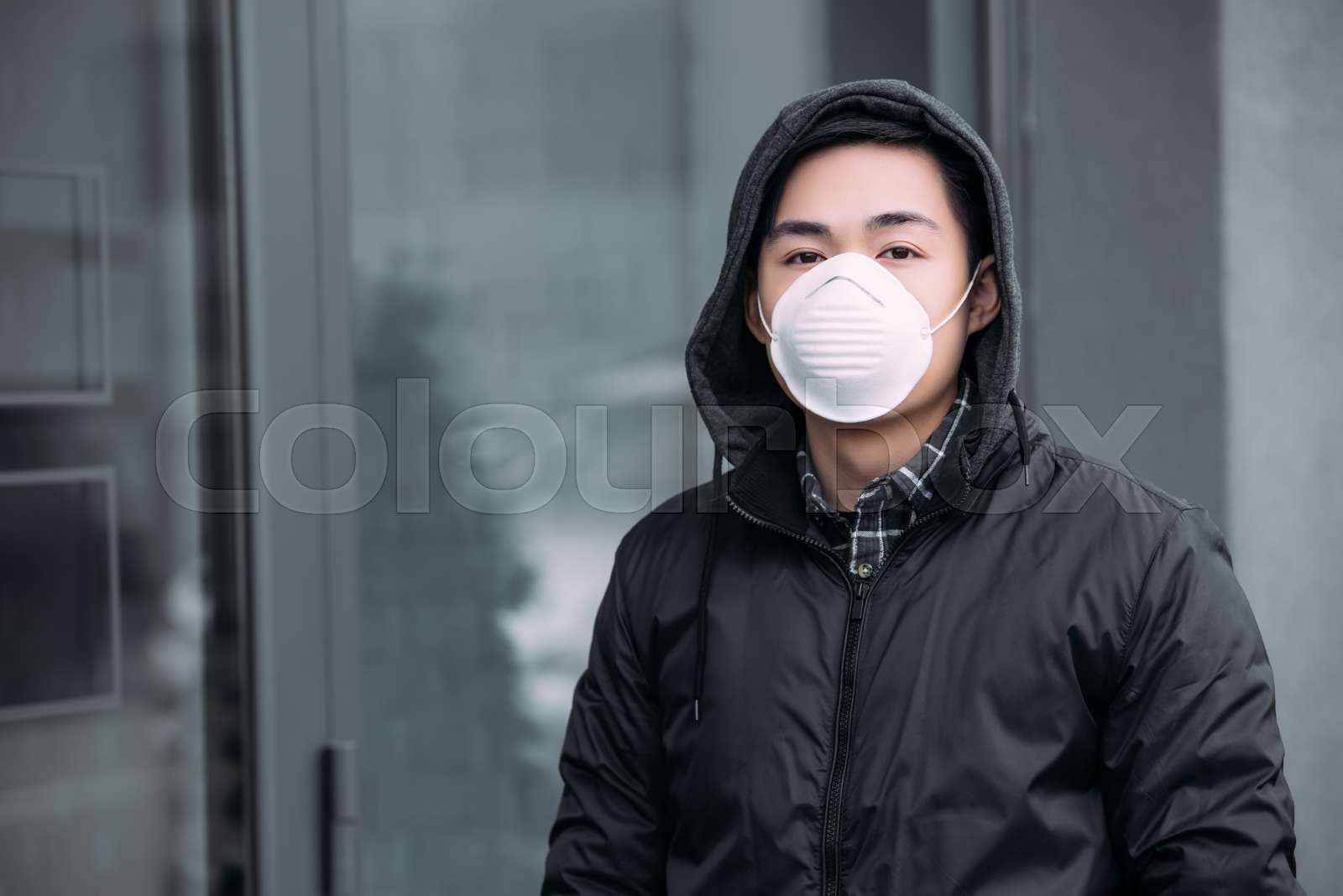 young asian man in respirator mask looking at camera while standing on ...