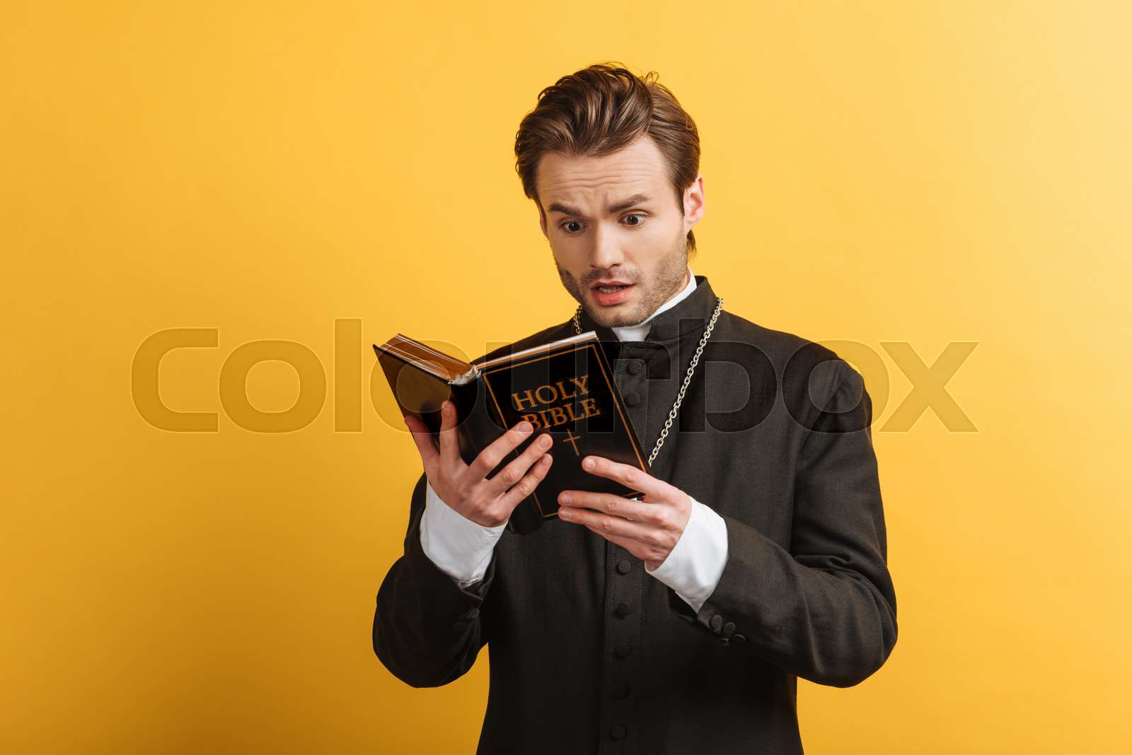 shocked catholic priest reading holy bible isolated on yellow | Stock ...