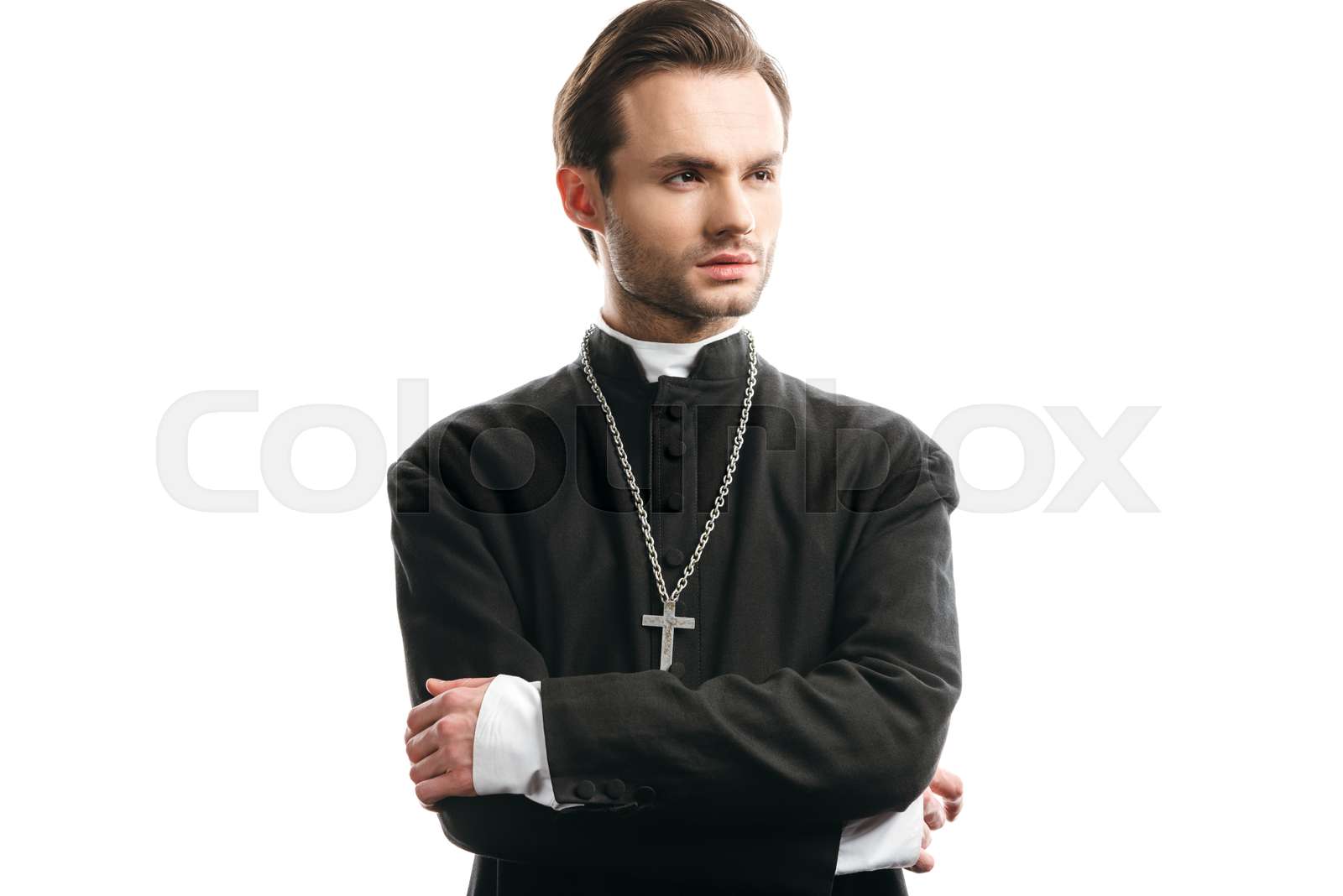 young, confident catholic priest looking away while standing with ...