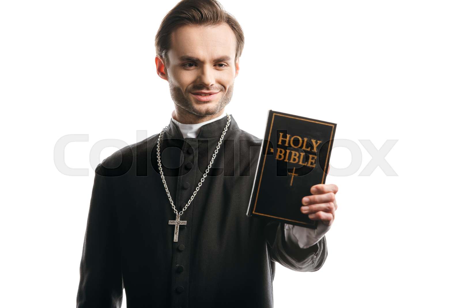 young catholic priest smiling while holding holy bible isolated on ...