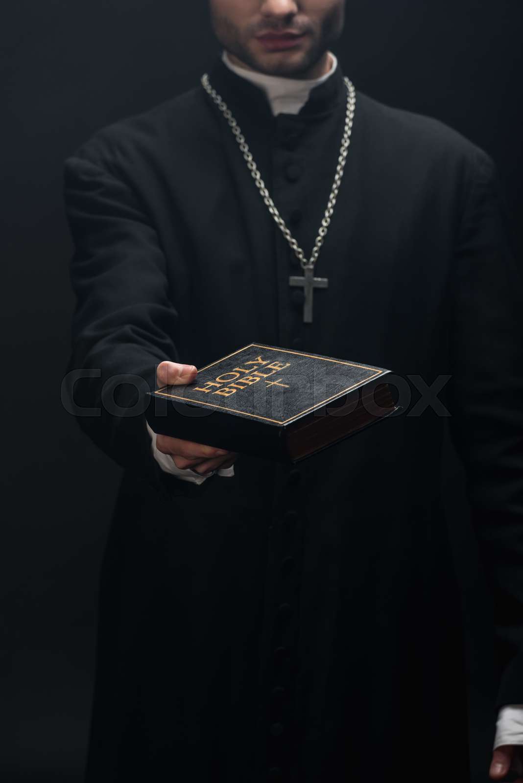 cropped view of catholic priest holding holy bible in outstretched hand ...