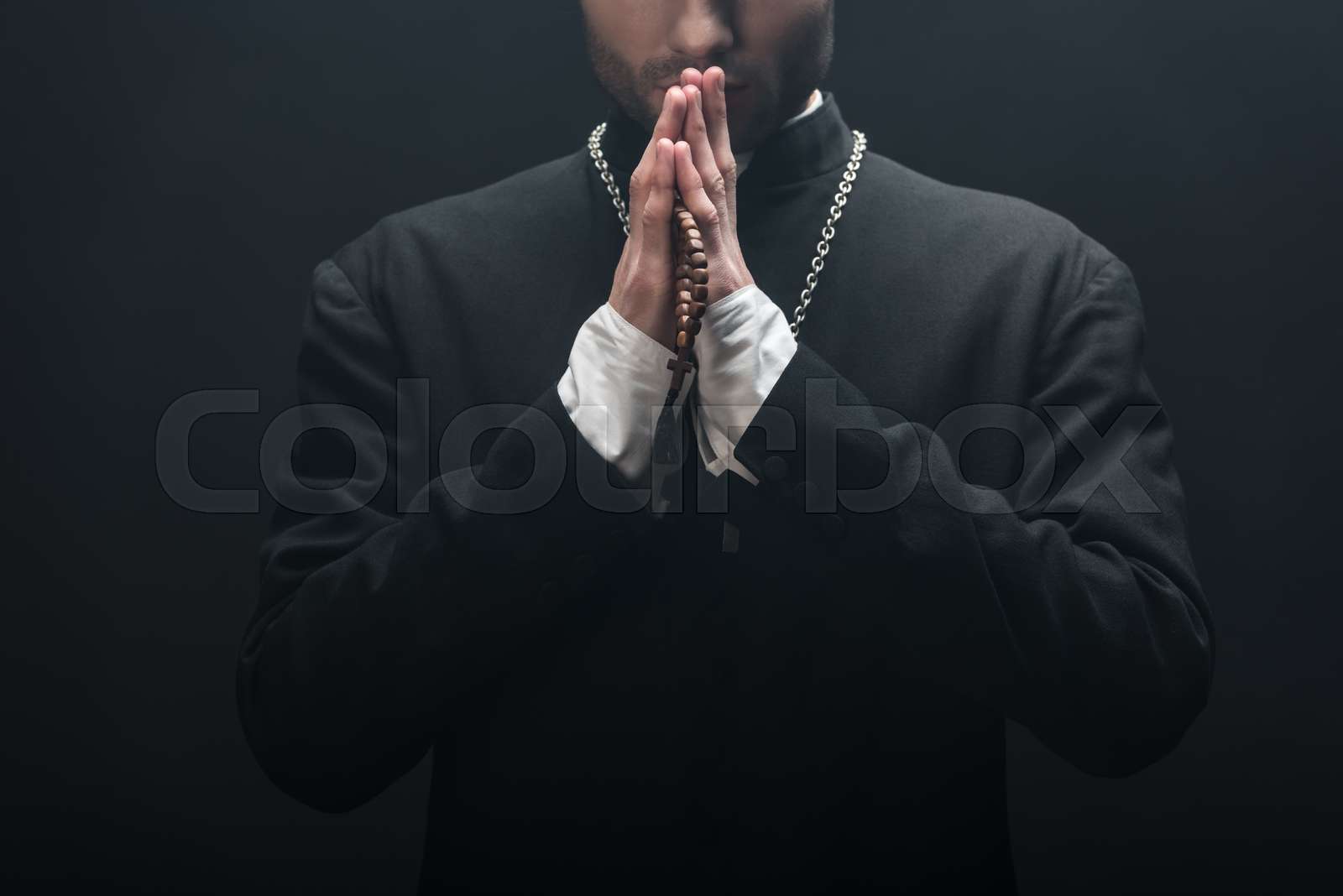 cropped view of young catholic priest praying isolated on black | Stock ...