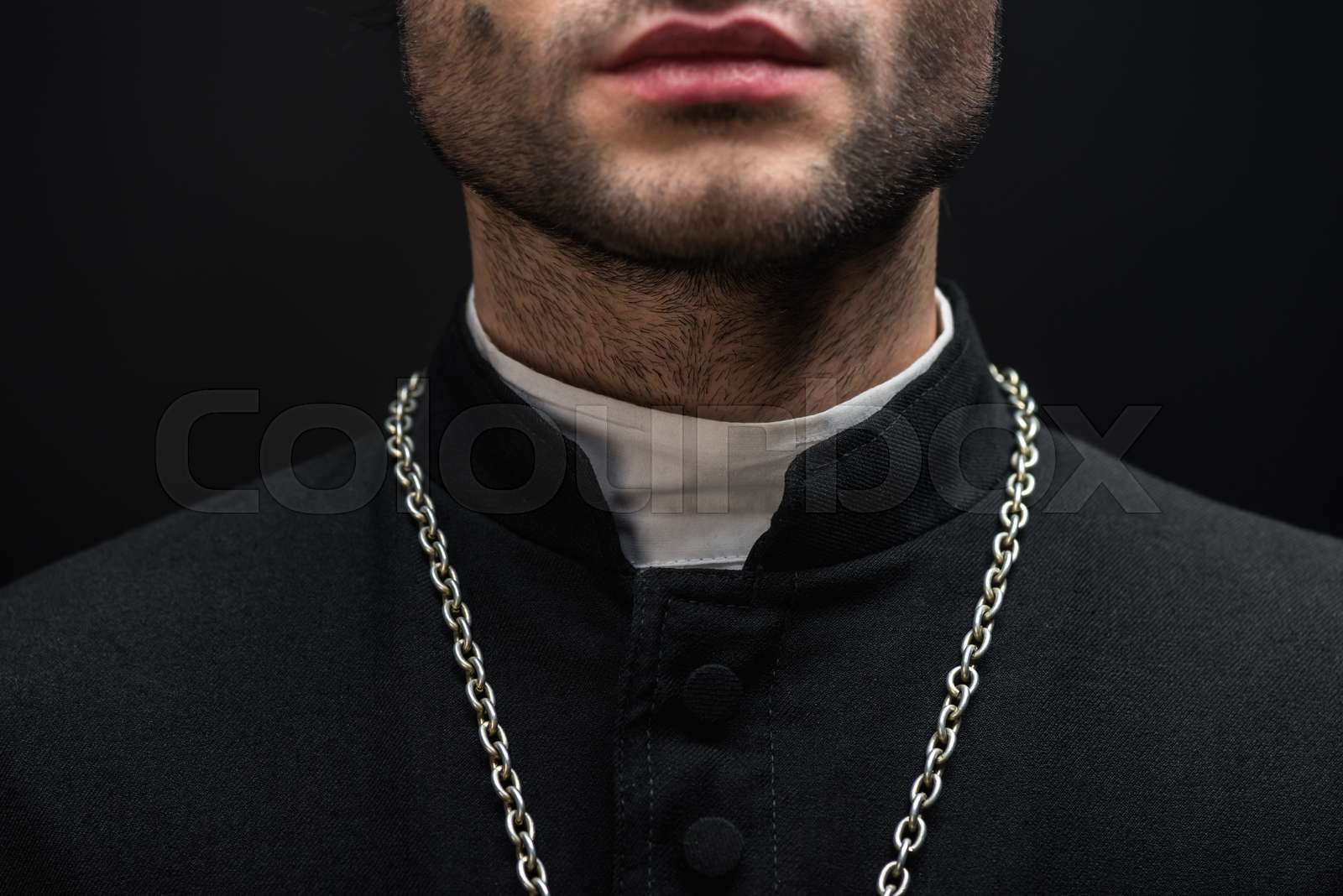 cropped view of catholic priest in black cassock with silver necklace ...