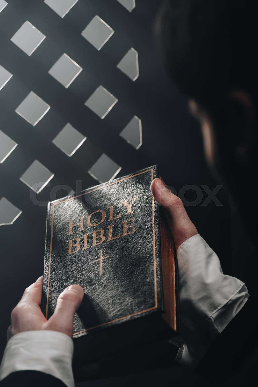 partial view of catholic priest holding holy bible near confessional ...