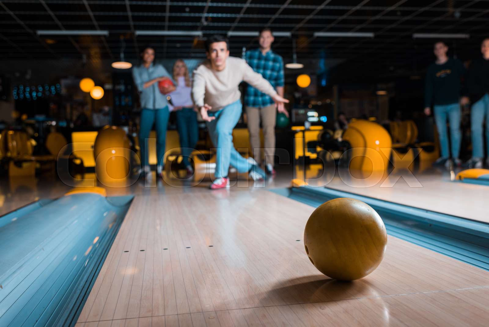 selective focus of young man throwing bowling ball on skittle alley ...