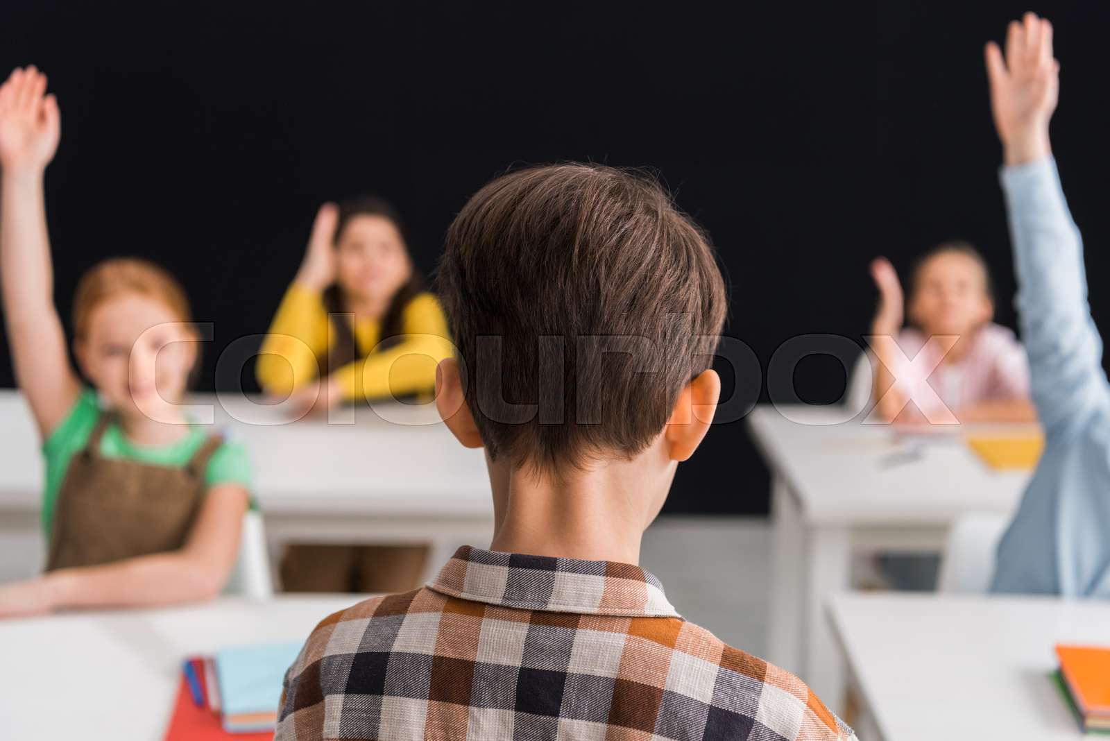 back view of schoolboy standing near classmates with raised hands ...