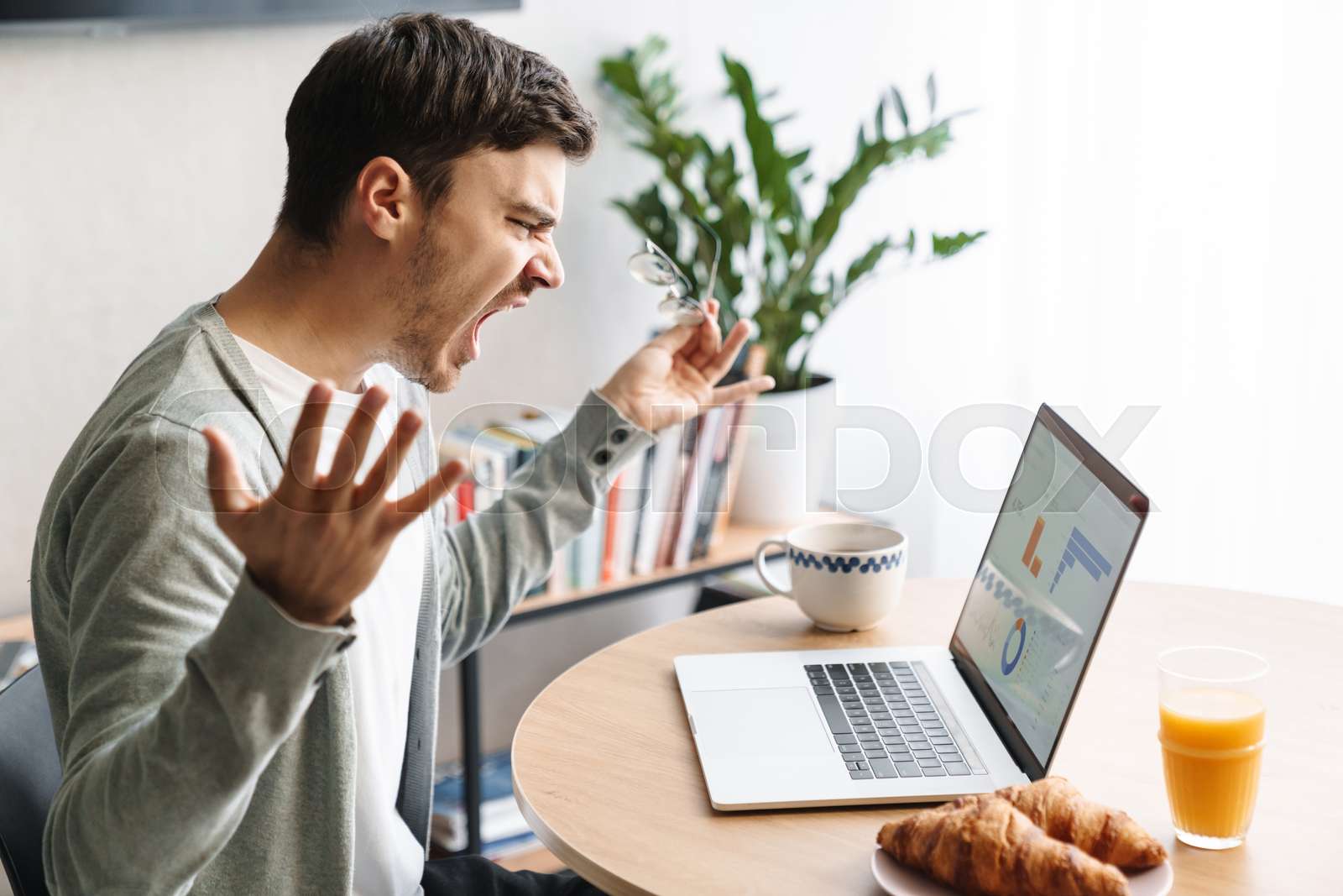 Image of angry young man screaming while working on laptop at home ...