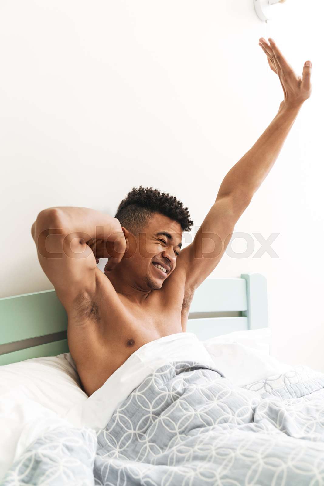 Guy in the morning in bedroom stretching in bed. | Stock image | Colourbox